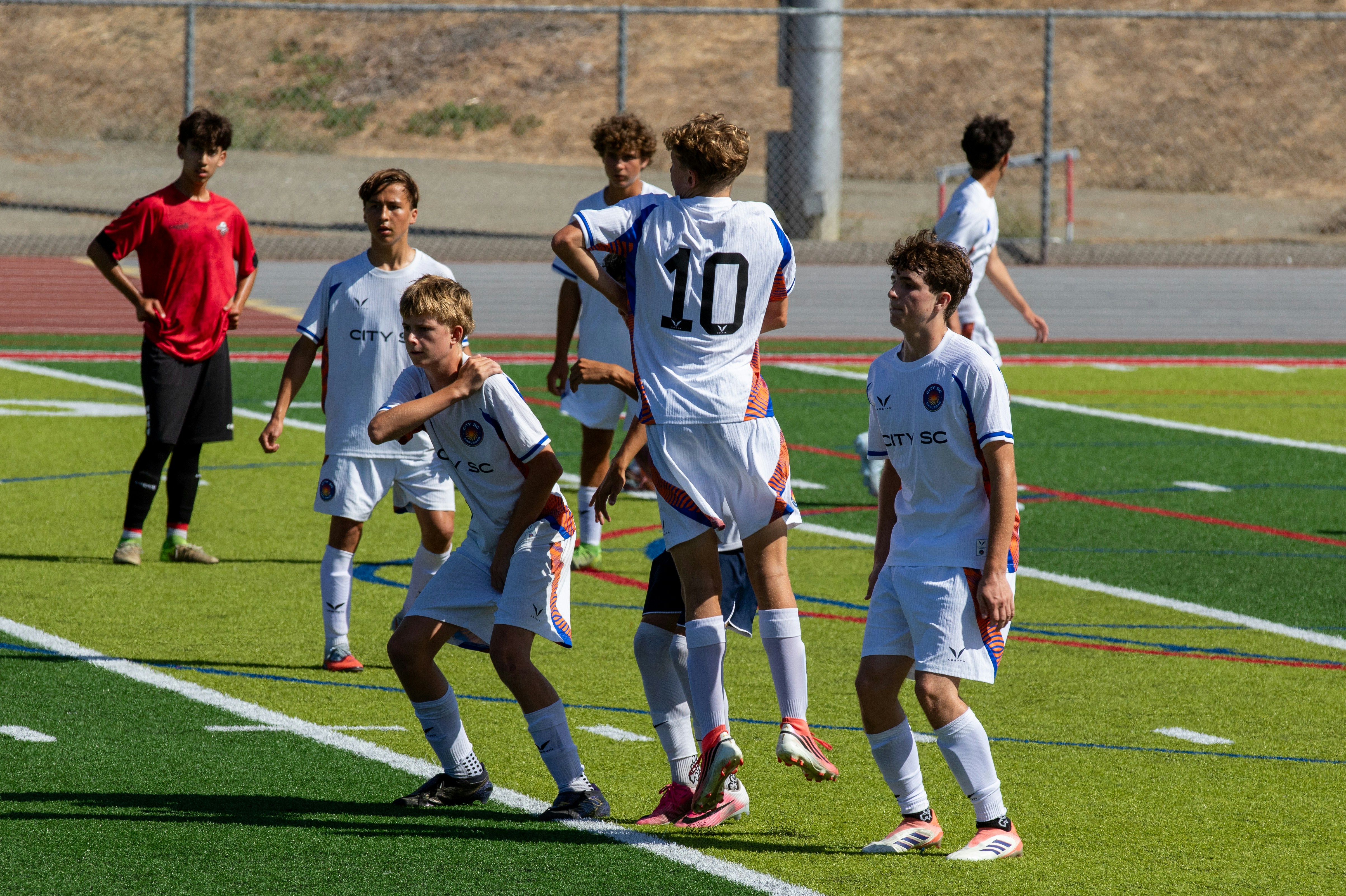 Team Huddle on the Grass: White Jerseys Converge as Play Builds
