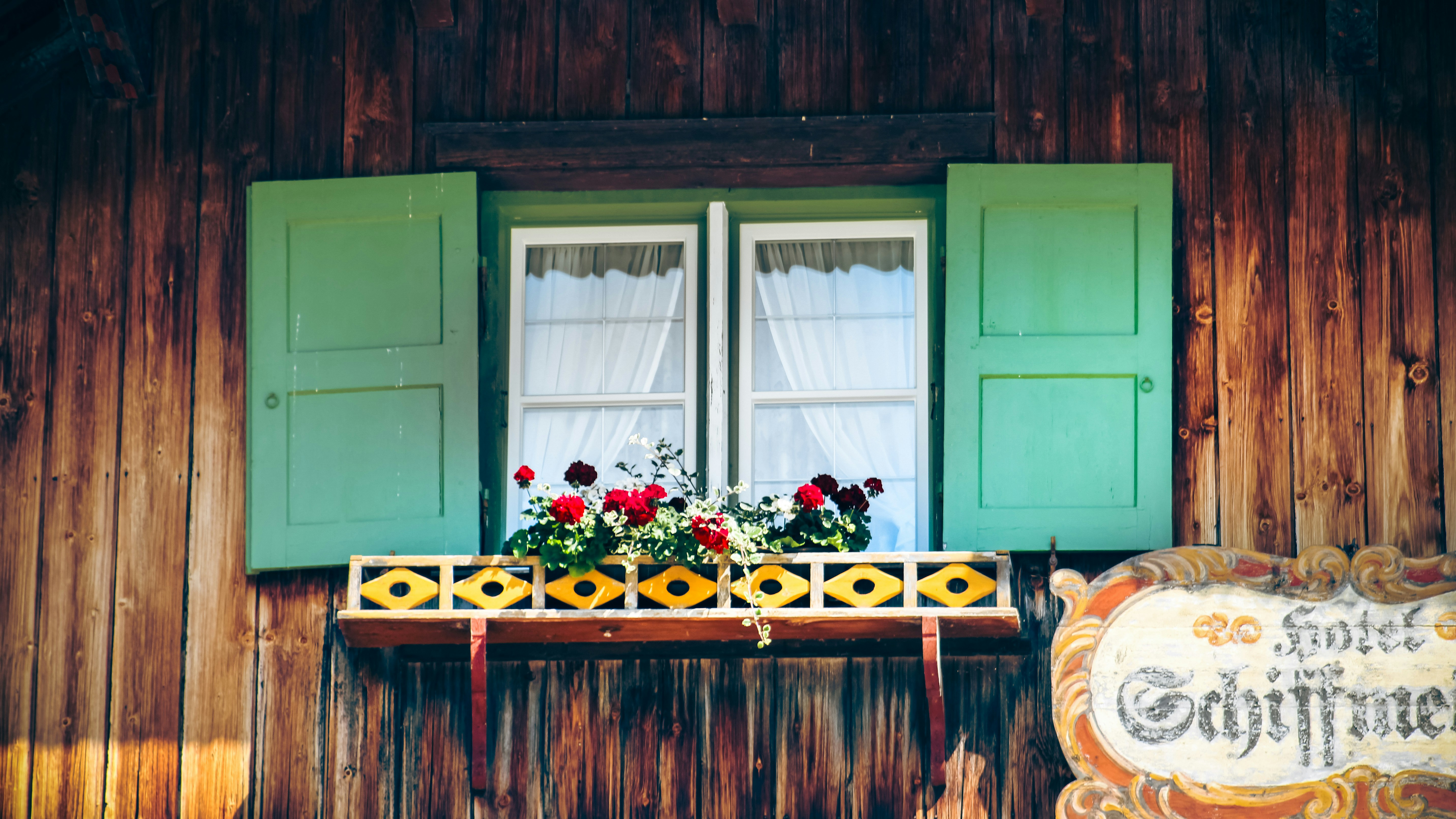 Green Shutter Window with Floral Balcony on Weathered Wood