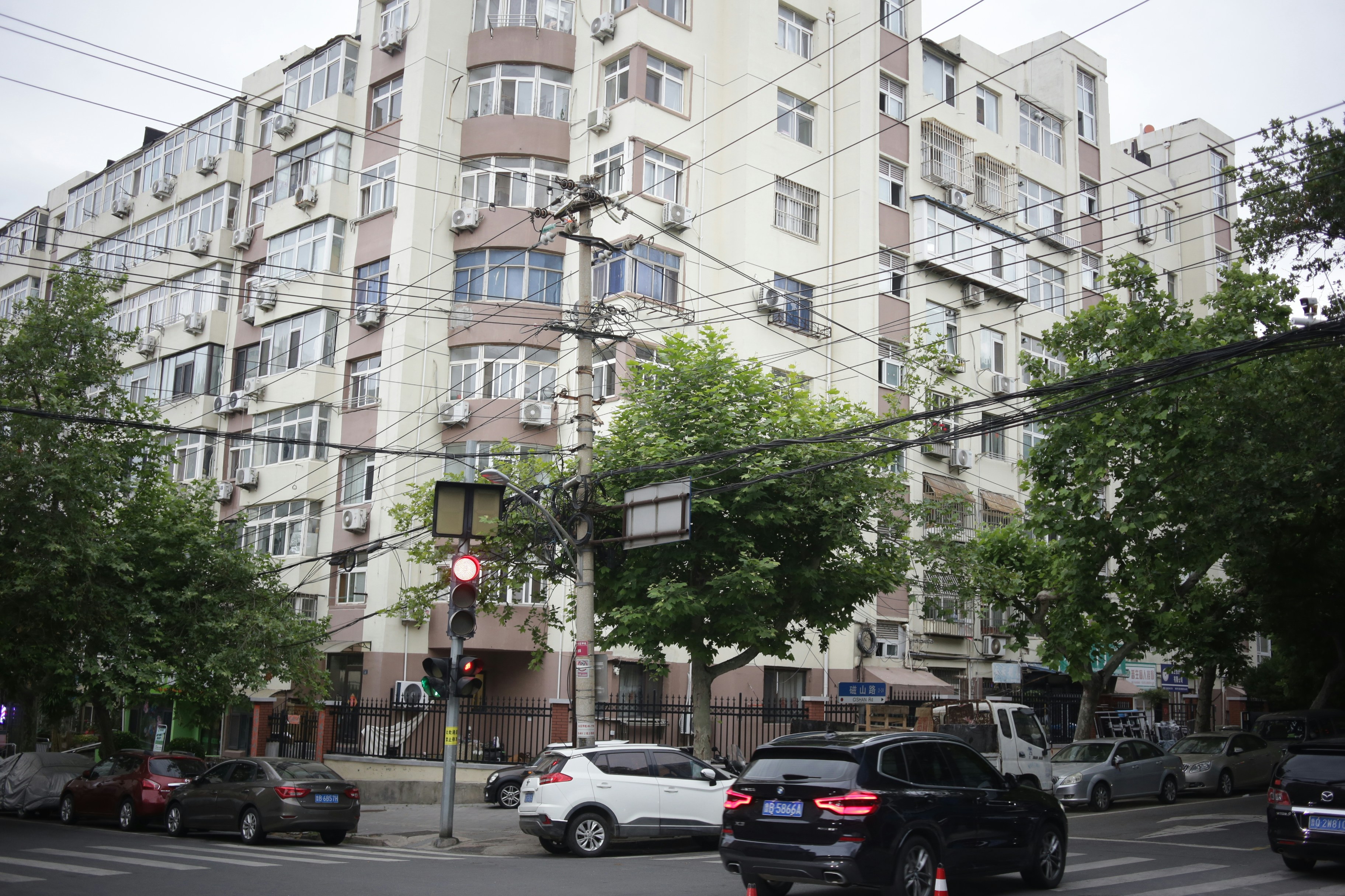 City Block Confluence: Cars Pause at a Tangle of Wires Before a Residential Facade