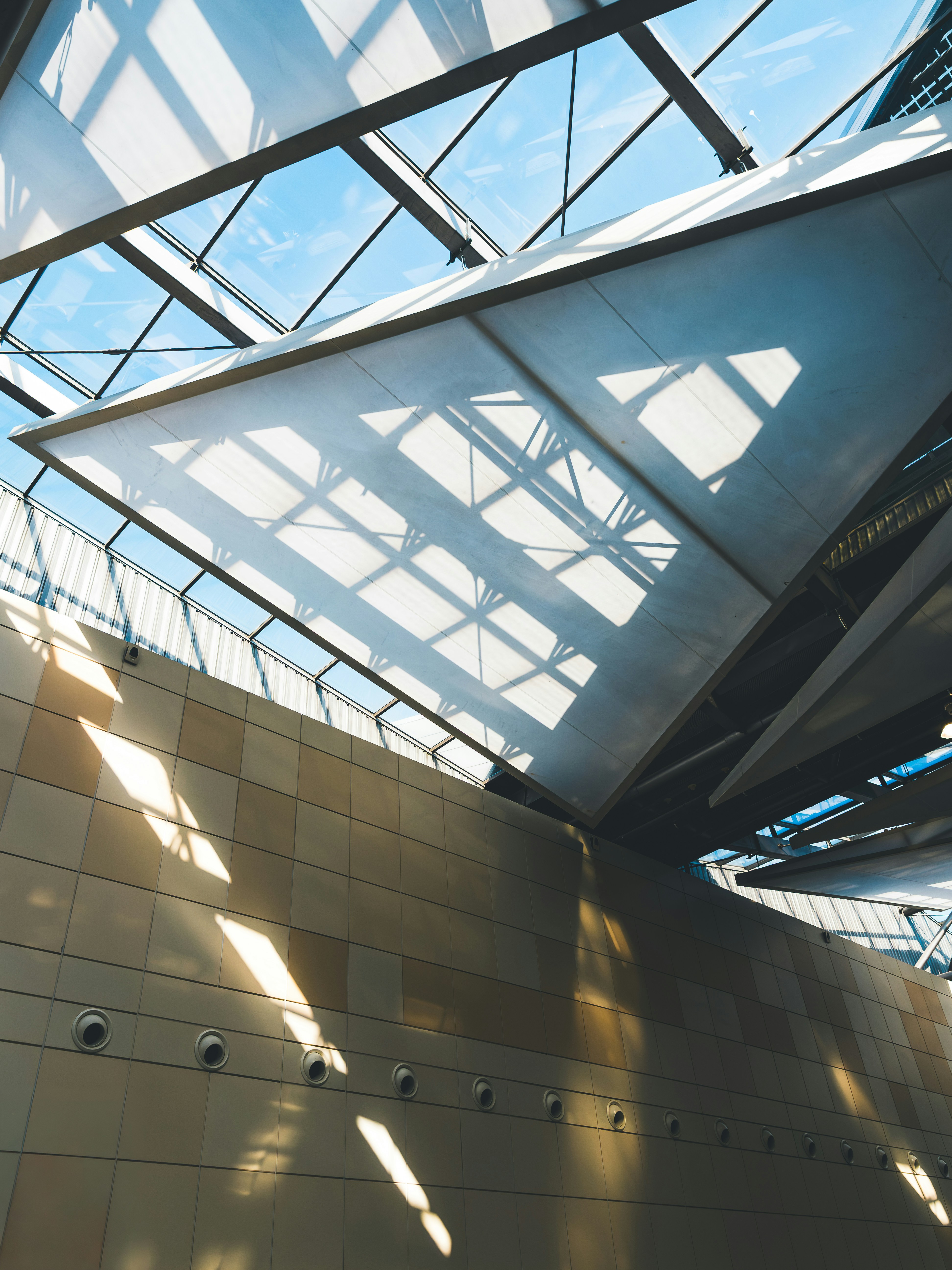 Intersecting Shadows: Glass Roof and Steel Beams Over a Monolithic Wall