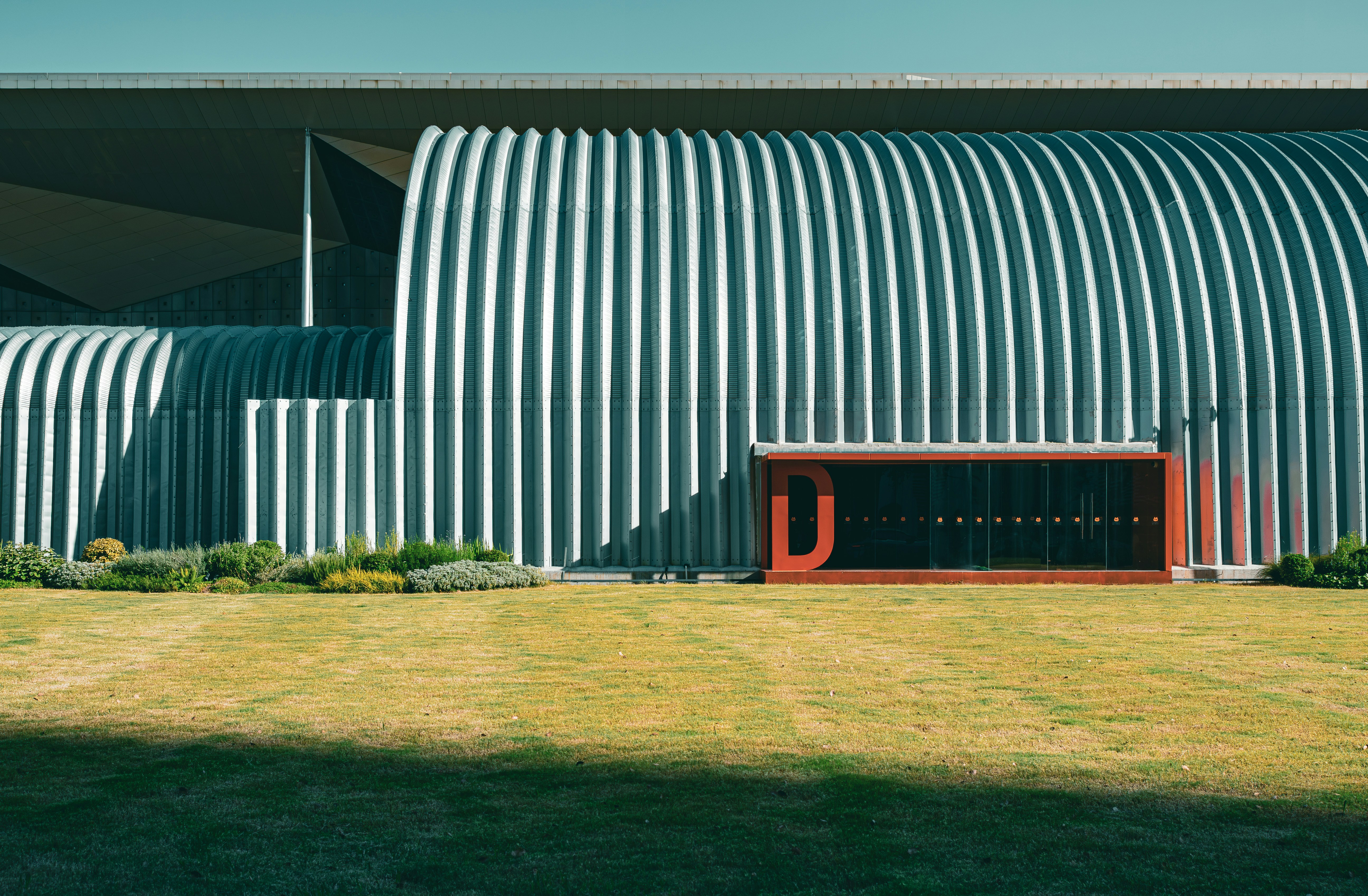 Curved Facade, Red Portal: Architecture in Sunlit Grass