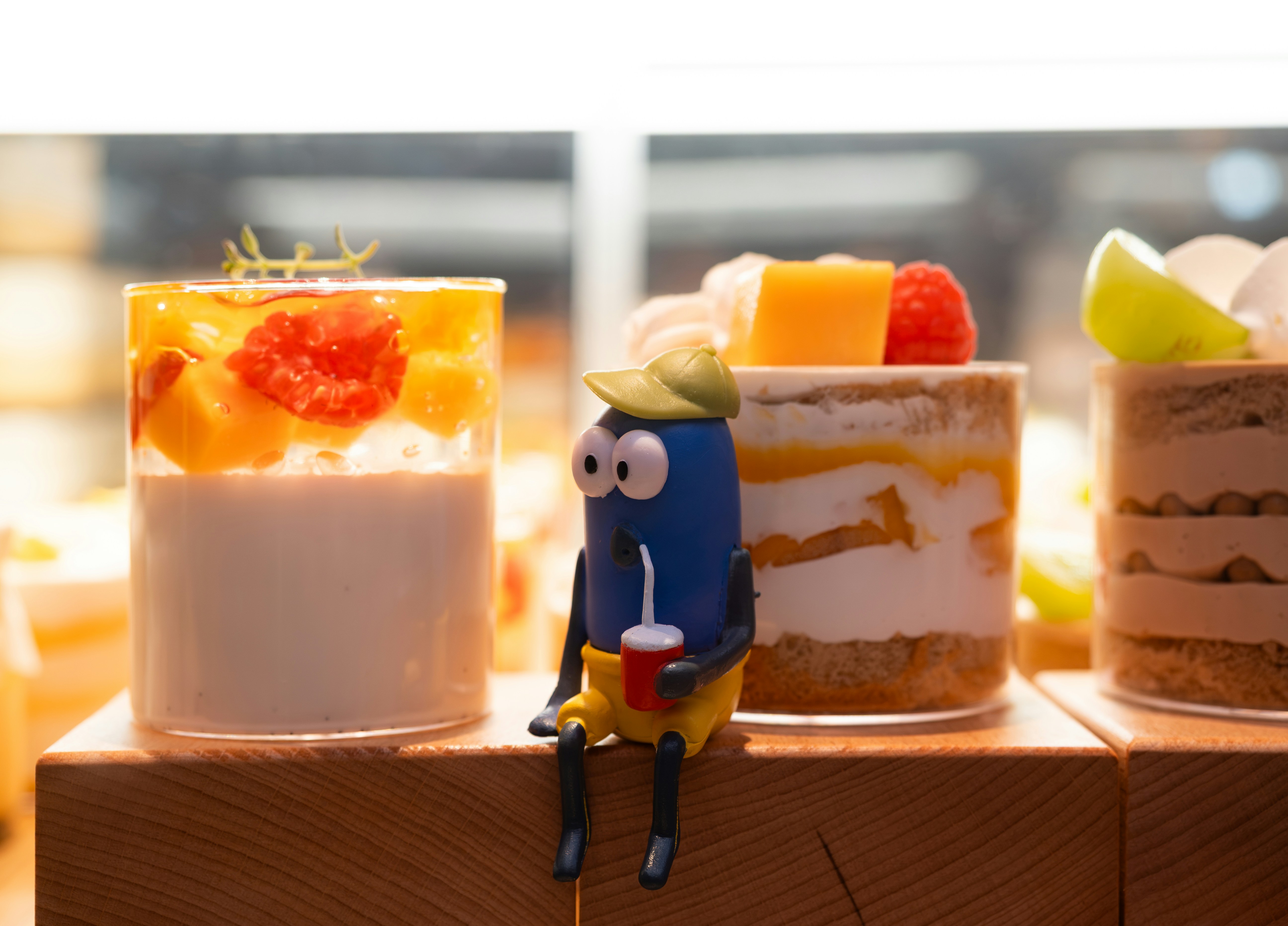 Blue clay character adrift among pastry towers on a wooden counter