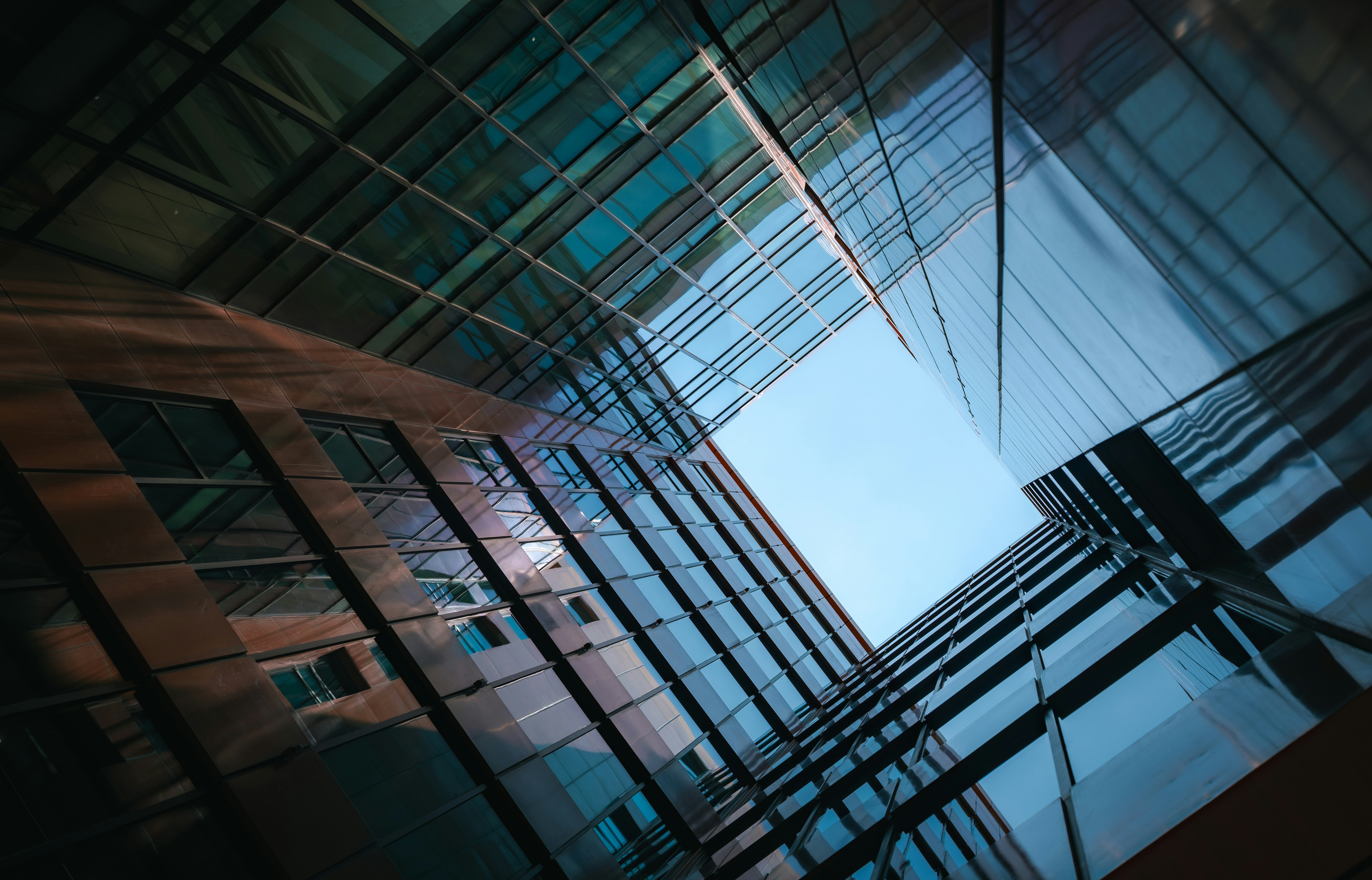 Angular glass towers tilt inward toward a bright core, creating a geometric canyon of reflections and blue tones. A modern atrium scene emphasizing perspective and vertical lines.