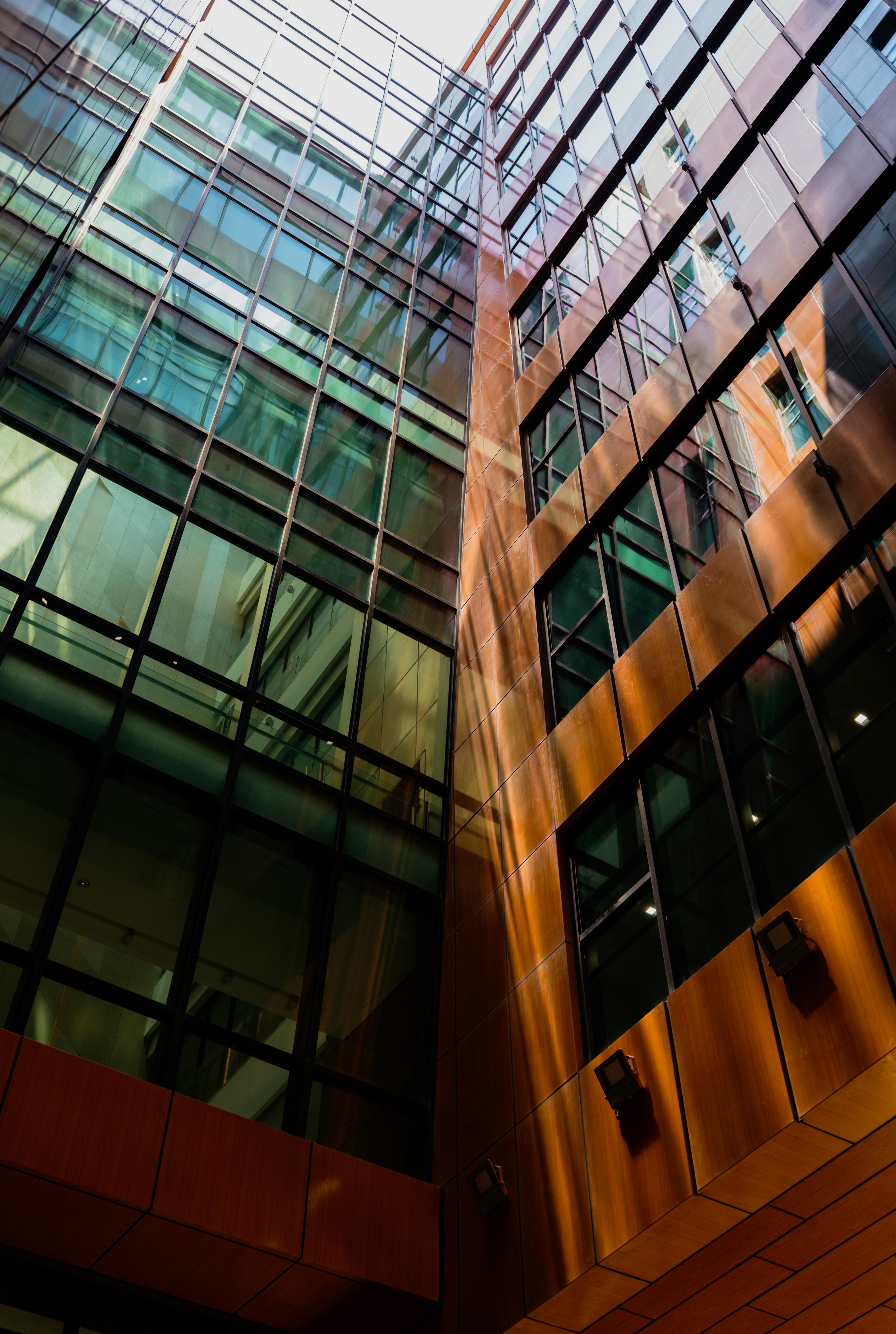 Sharp, angled perspective of a modern glass-and-copper facade with intersecting lines and reflections, highlighting architectural craft and color contrasts. This is a architectural photography shot.