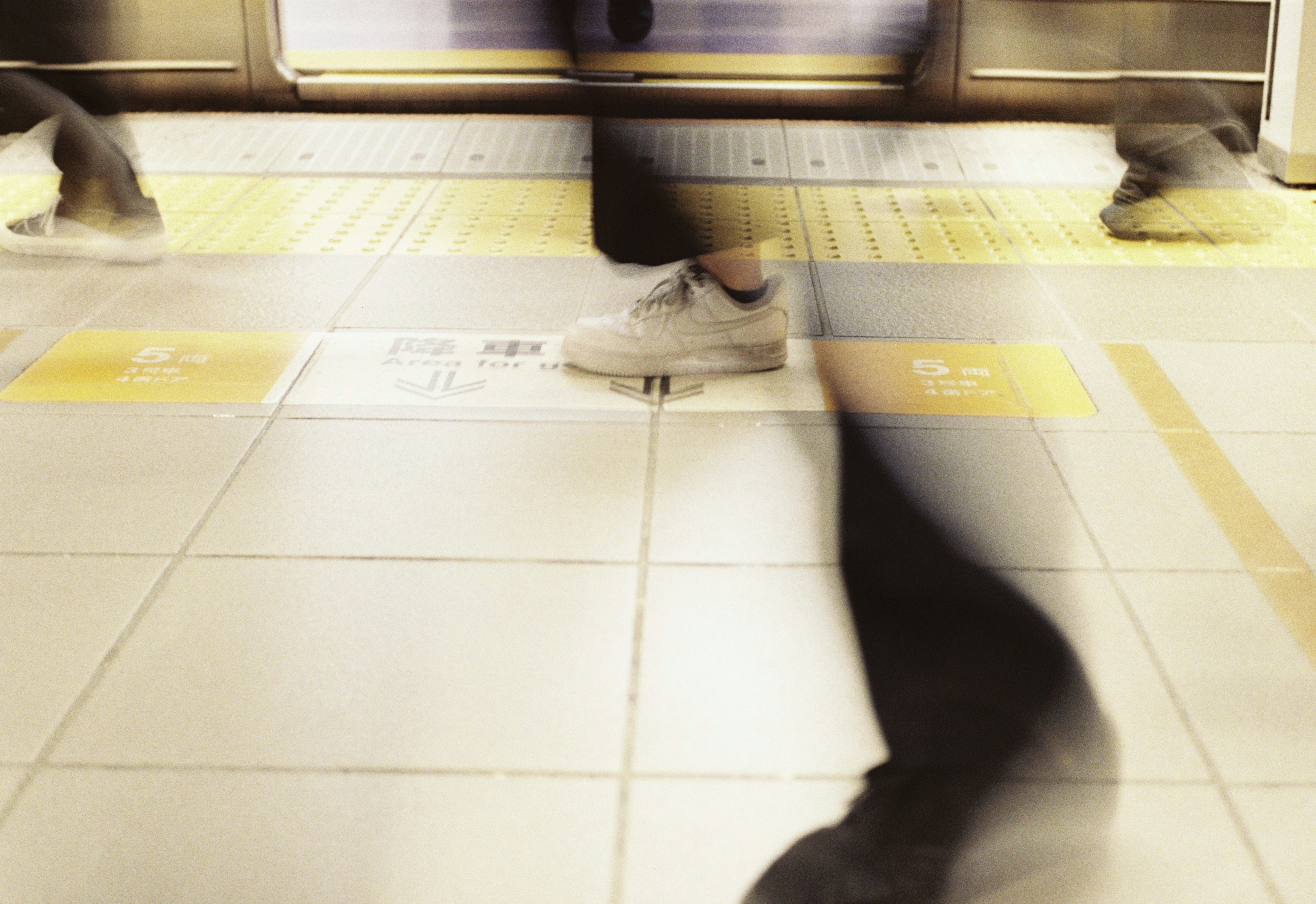  commuters rush along a station platform as a runner strides through the frame, the shallow depth of field and warm tones emphasizing transit motion.