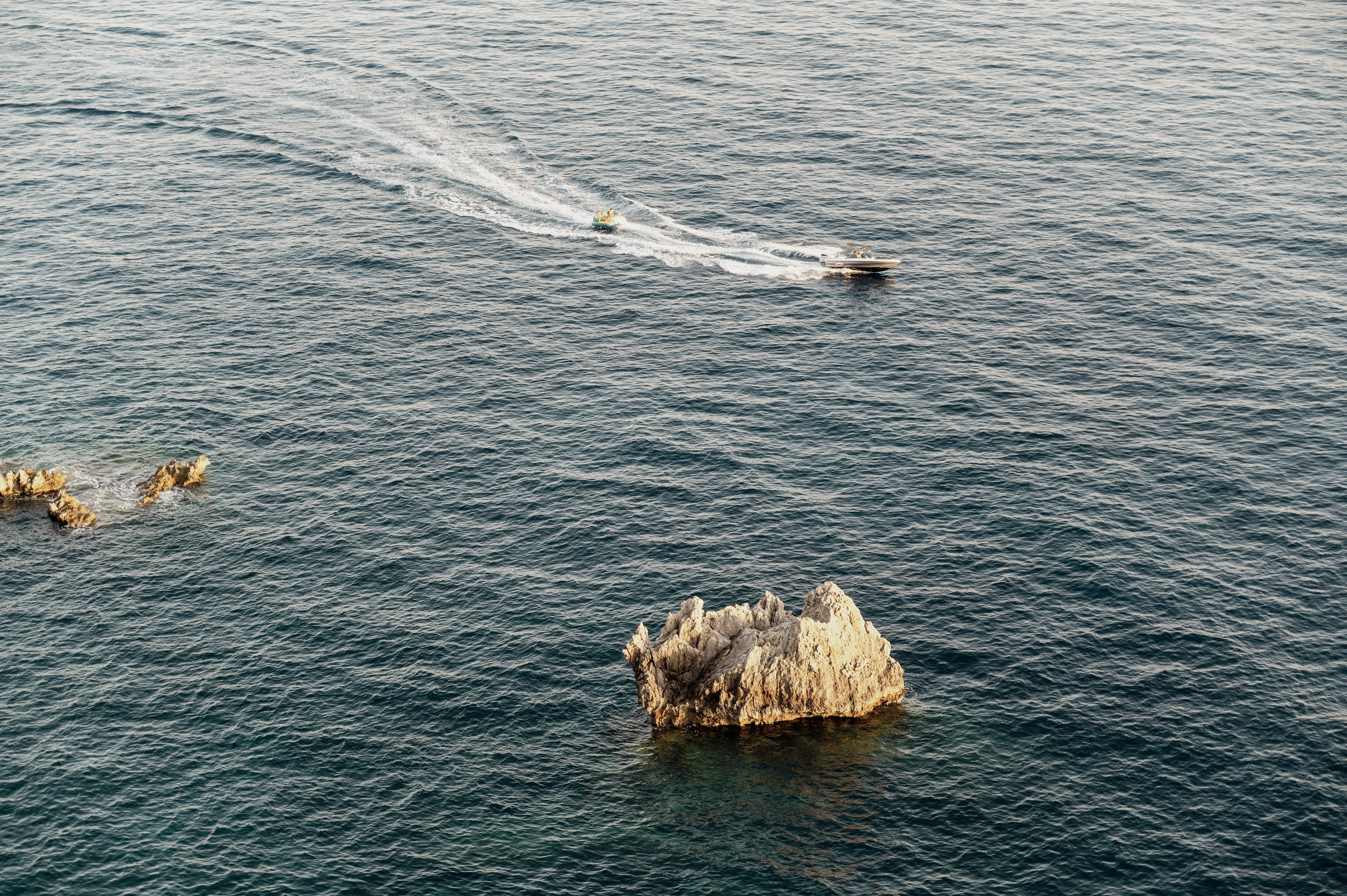 Coastal wake: speedboat carving a path past sunlit sea stacks