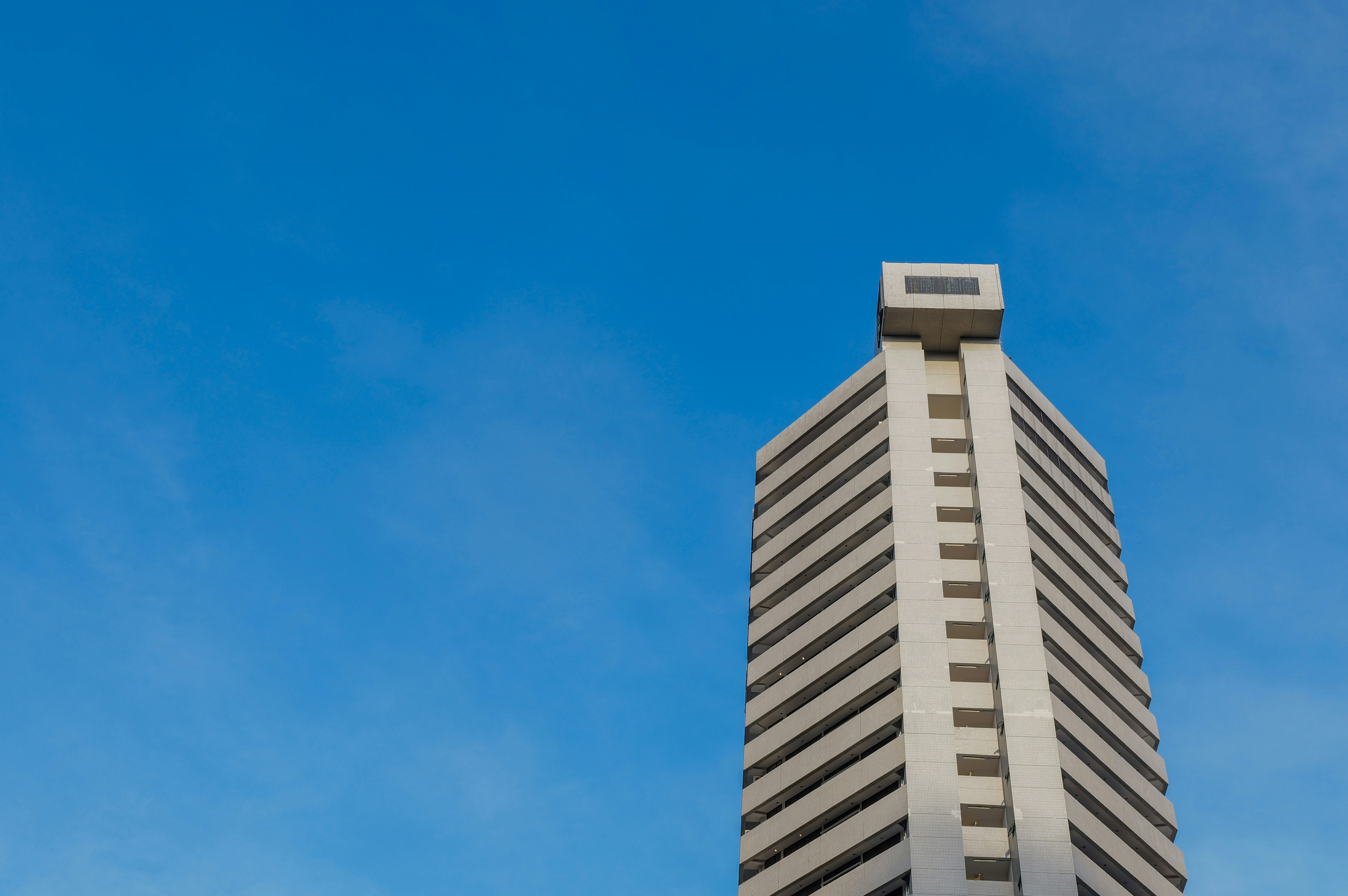 Crisp portrait of a modern high-rise piercing a clear blue sky with strong geometric lines and shadowed recesses.