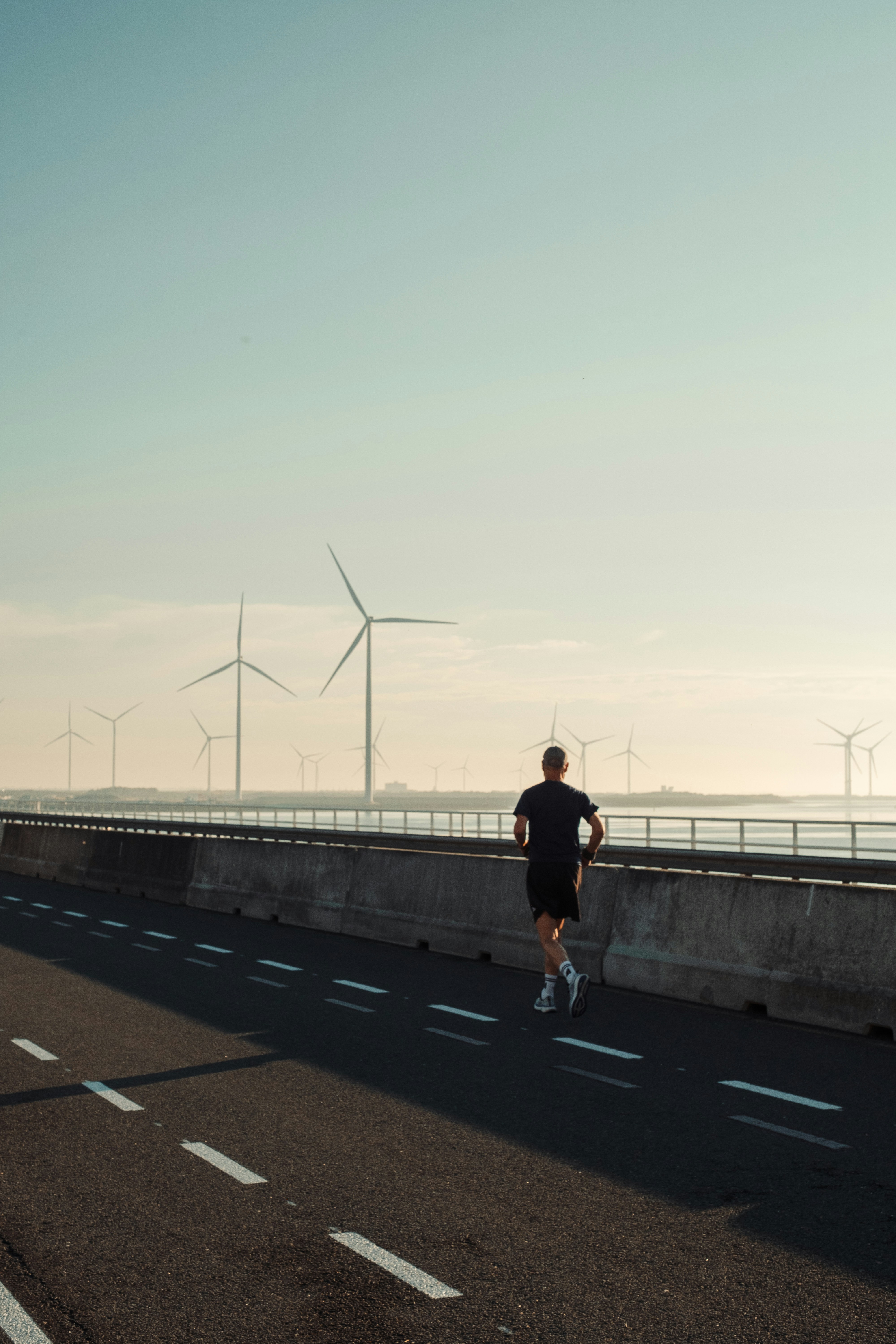 Runner on a Wind-Swept Highway toward Distant Turbines