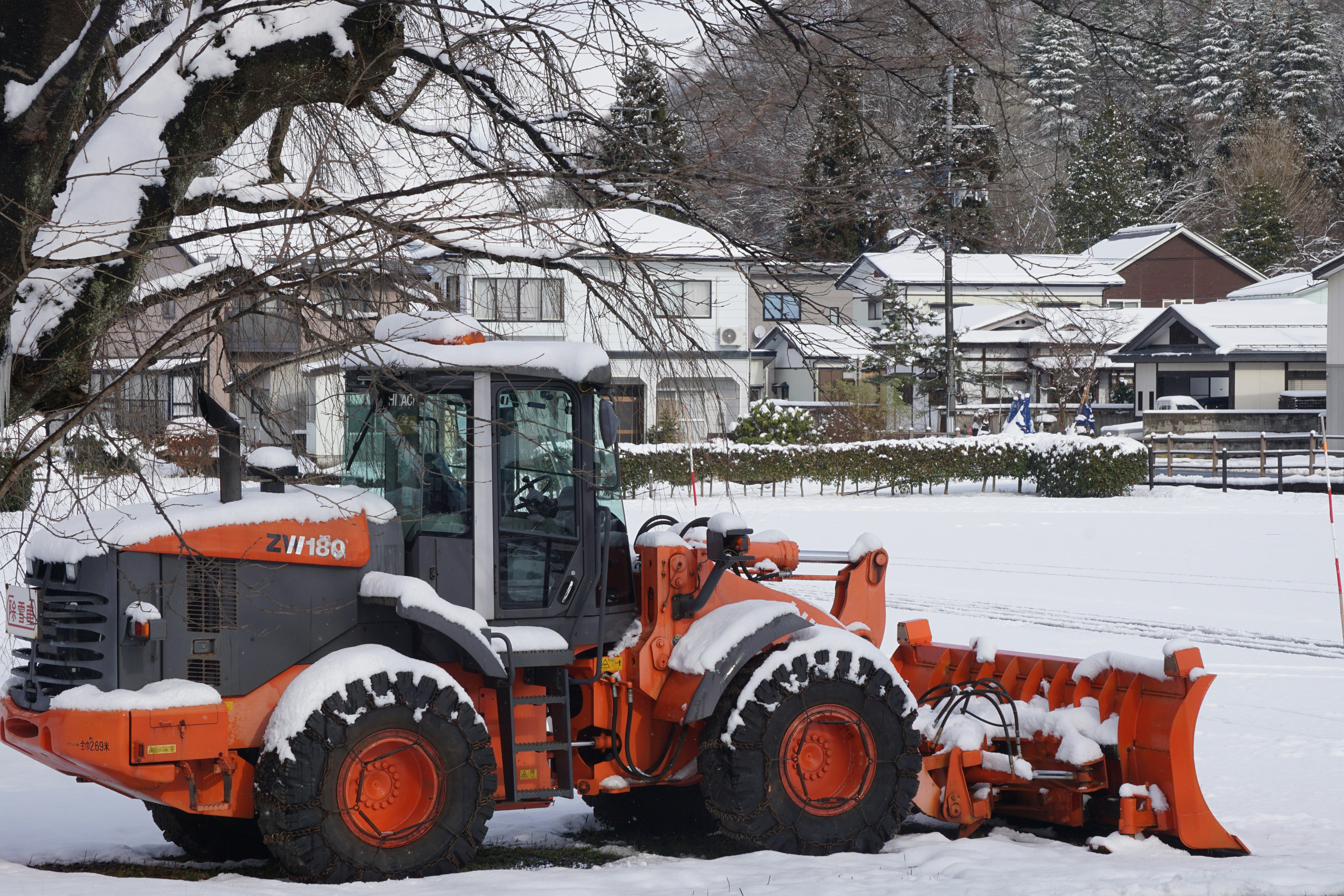 Orange Snowplow at Rest in Quiet Snow-Covered Suburban Street