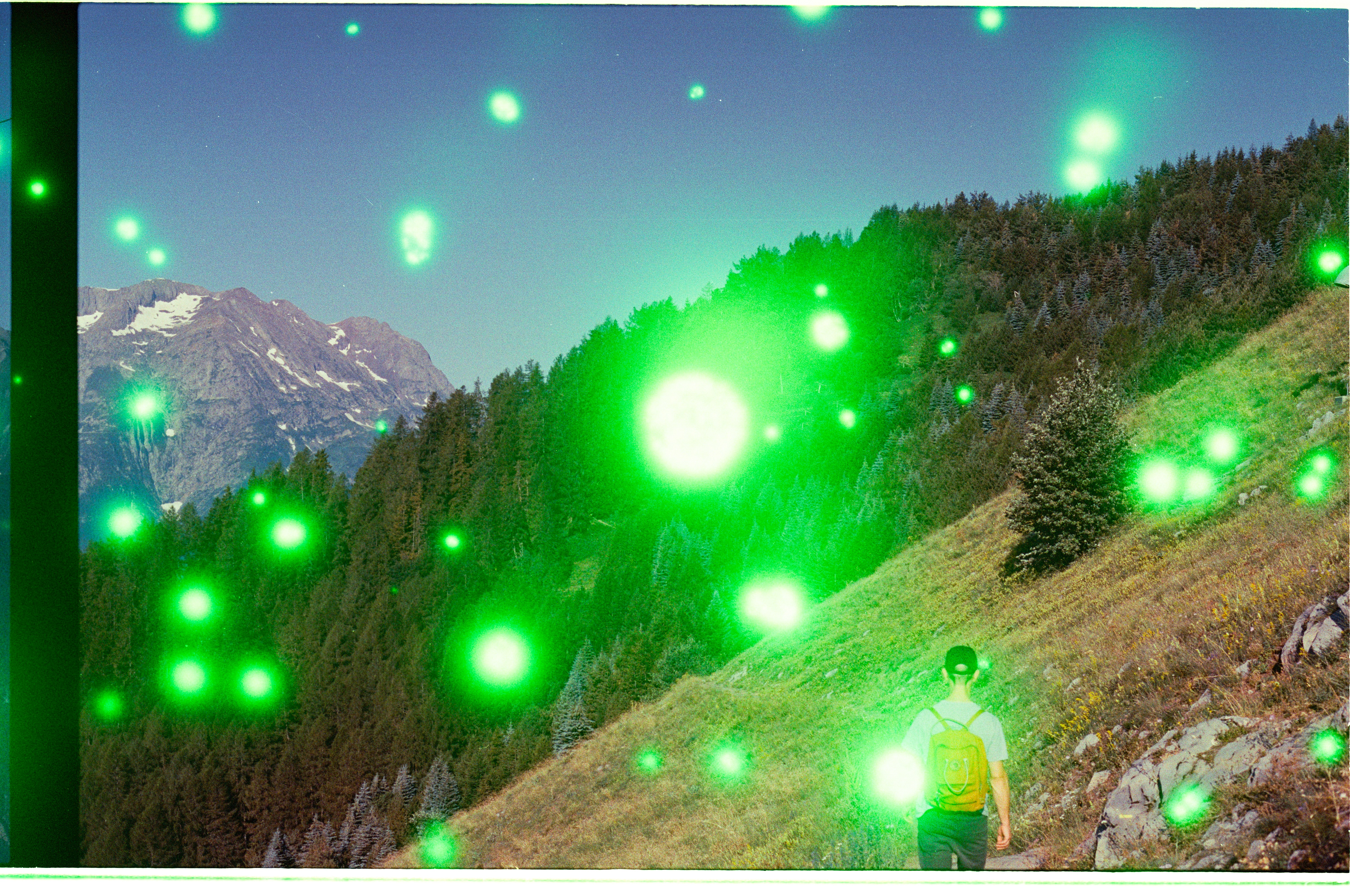 Green orbs over alpine trail: a solitary hiker beneath a night-sky glow