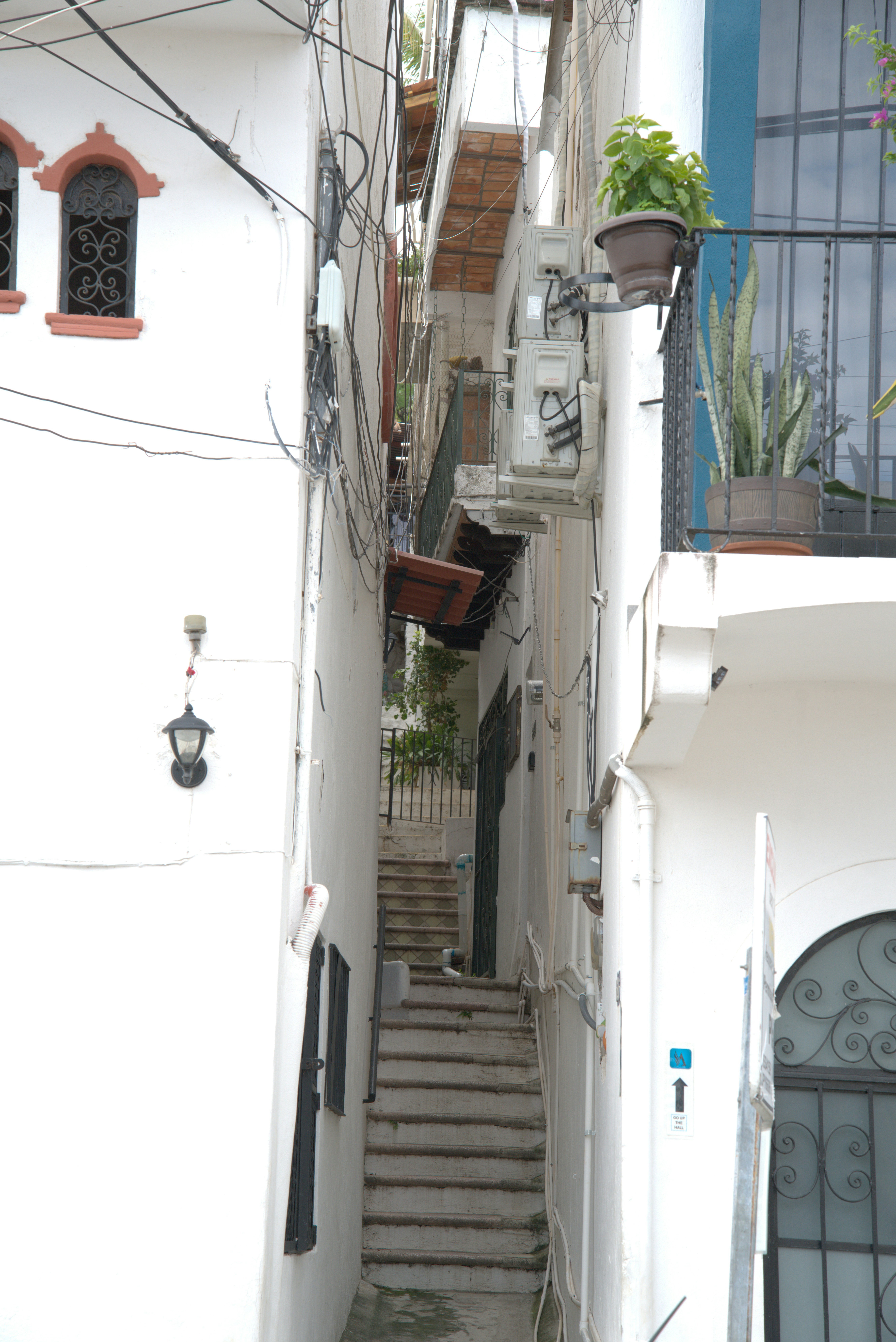 Narrow stairwell shrine: a sunlit alleyway climbing toward a hidden courtyard