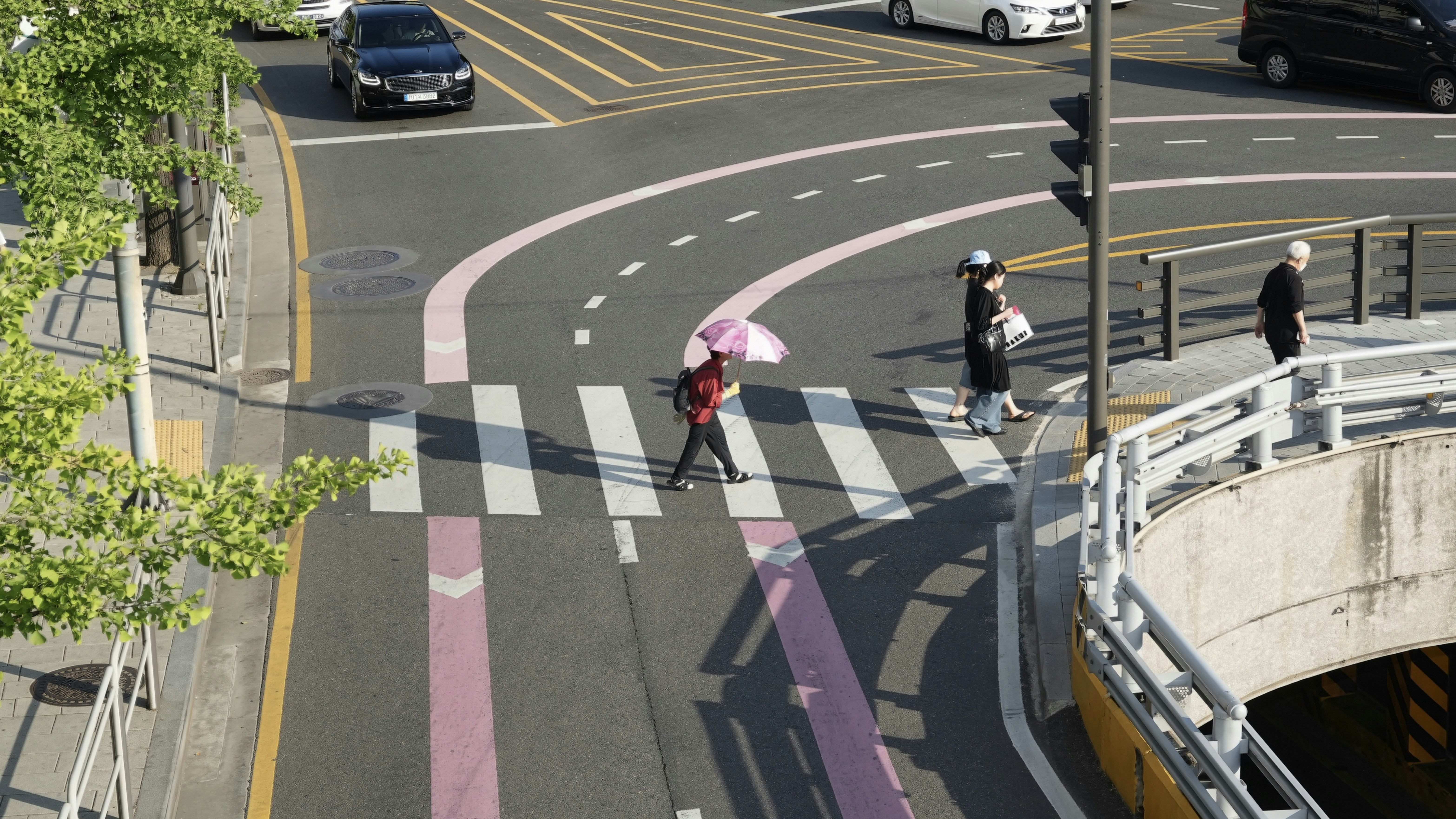 Three pedestrians cross a multi-lane street at a modern intersection with vibrant crosswalk and painted curves.