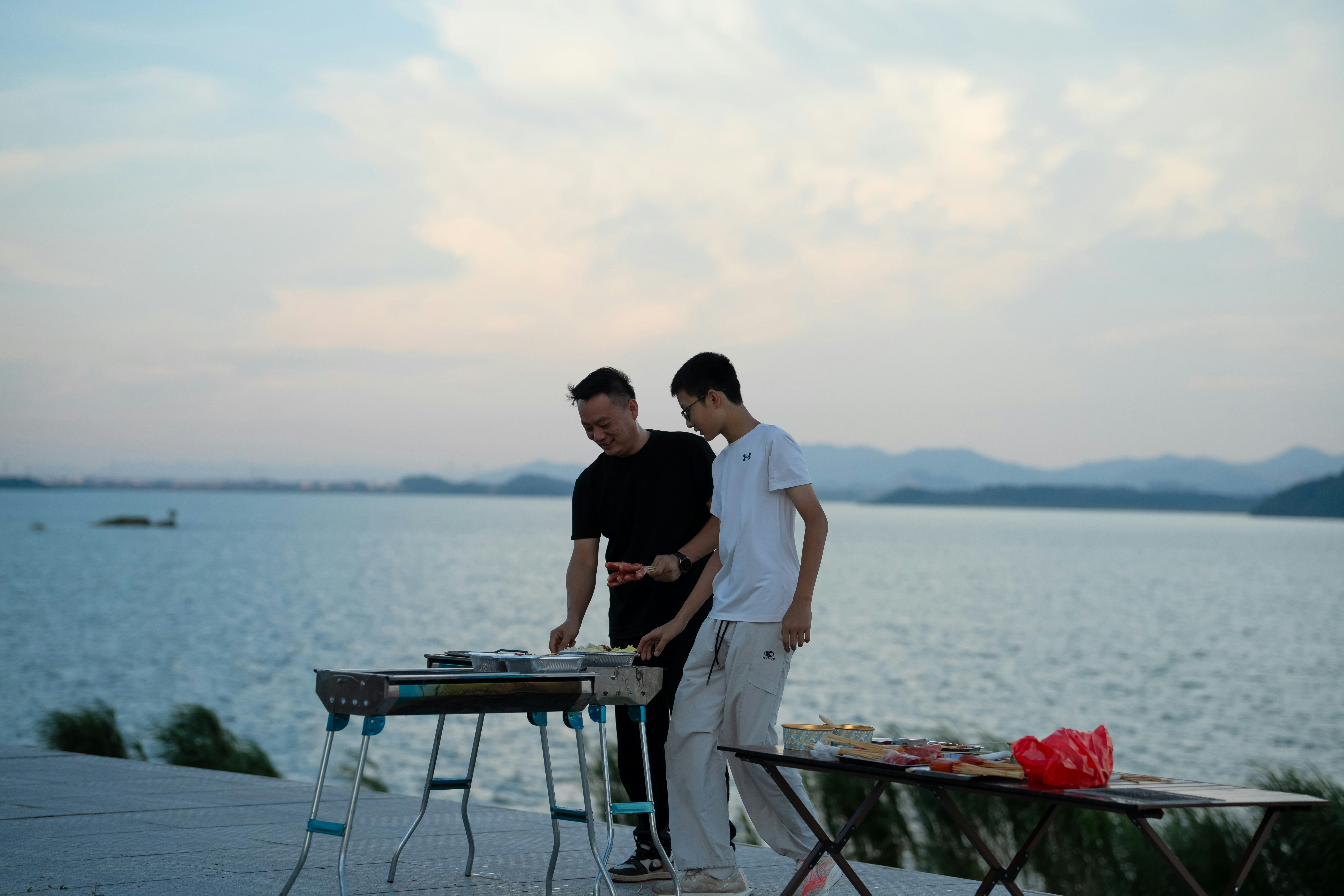 Two friends BBQ by the calm lakeside at golden hour