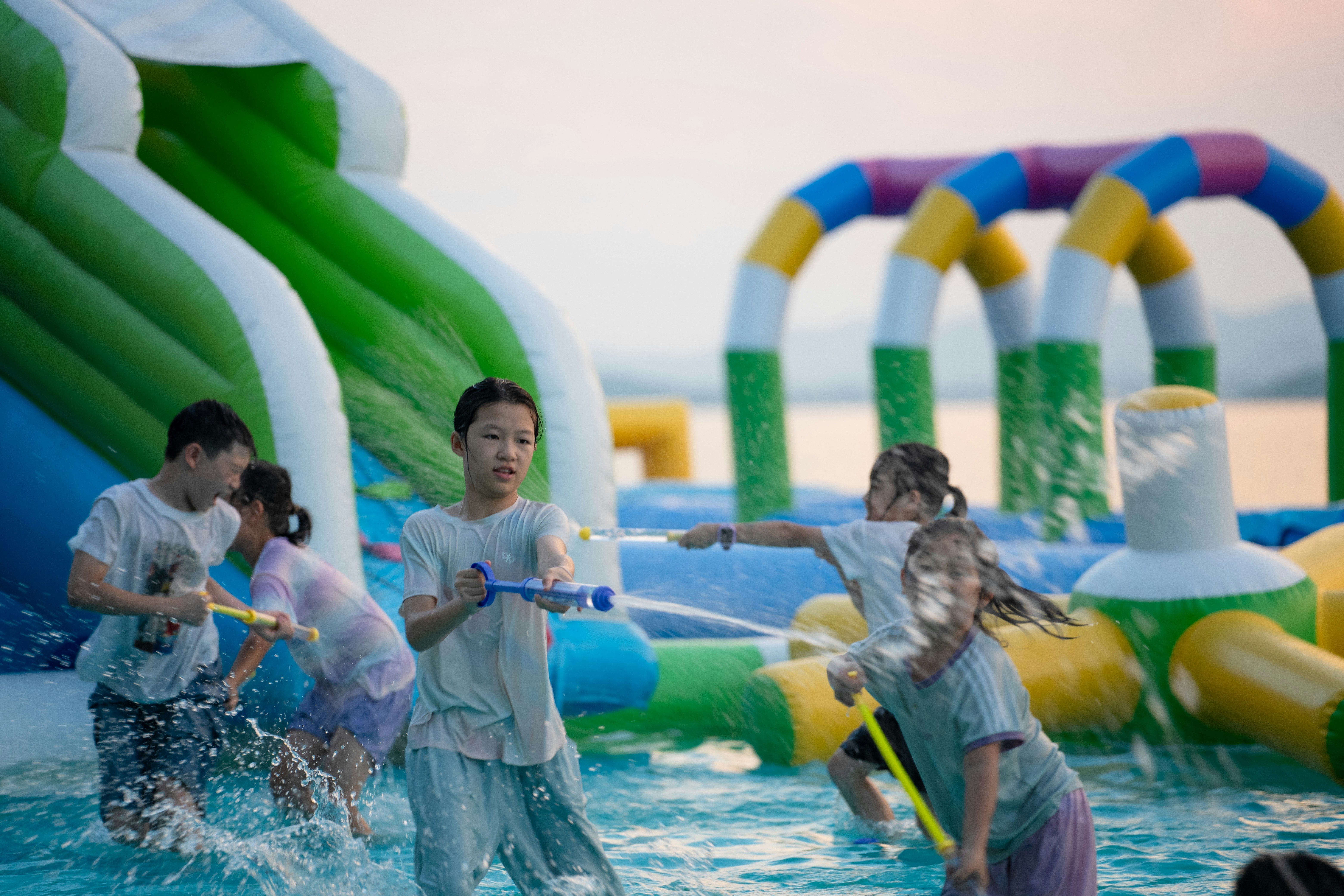 Liquid Lagoon Skirmish: Kids With Water Blasters at a Sunlit Inflatable Park