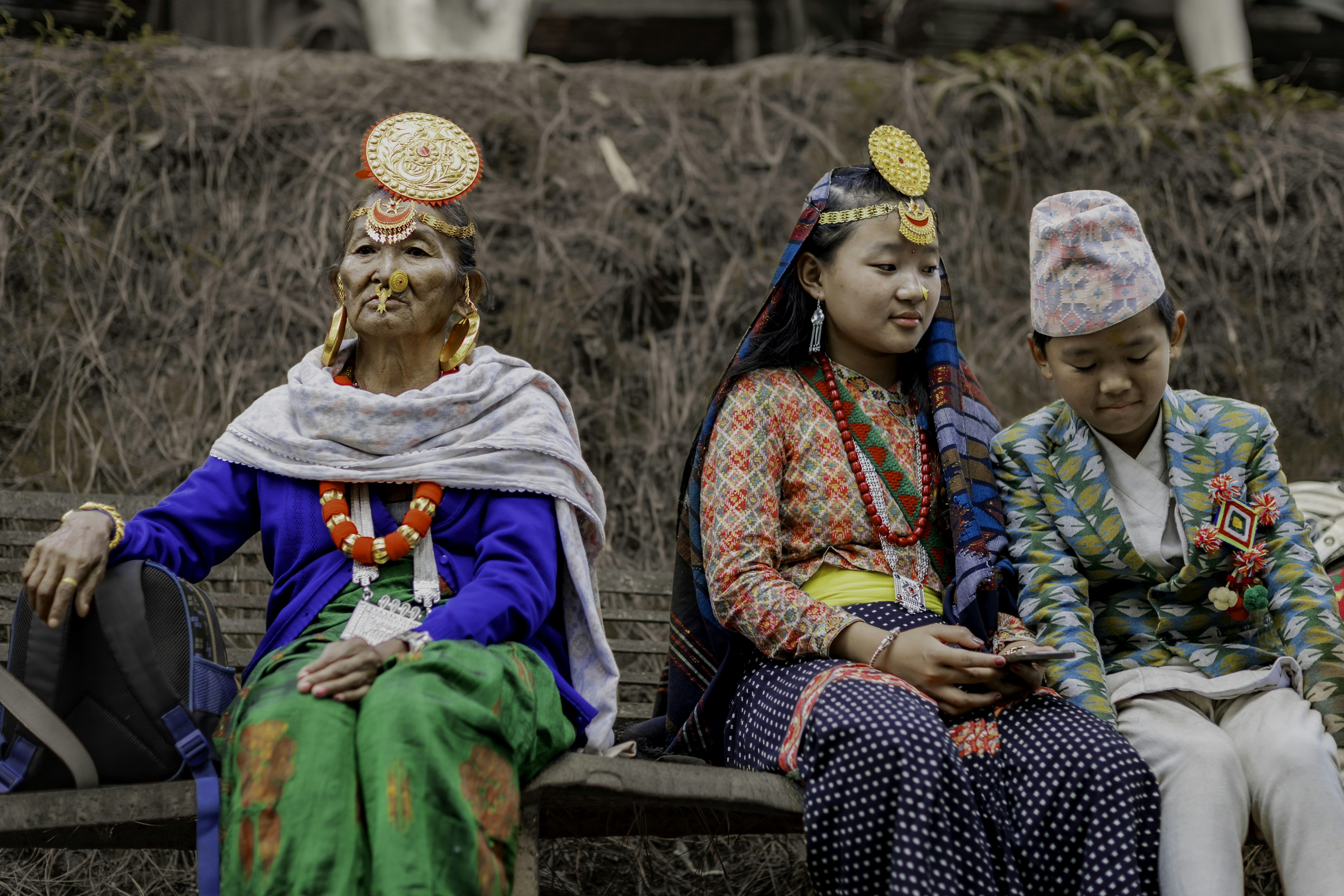 Three Generations in Traditional Regalia Share a Quiet Moment on a Rustic Bench