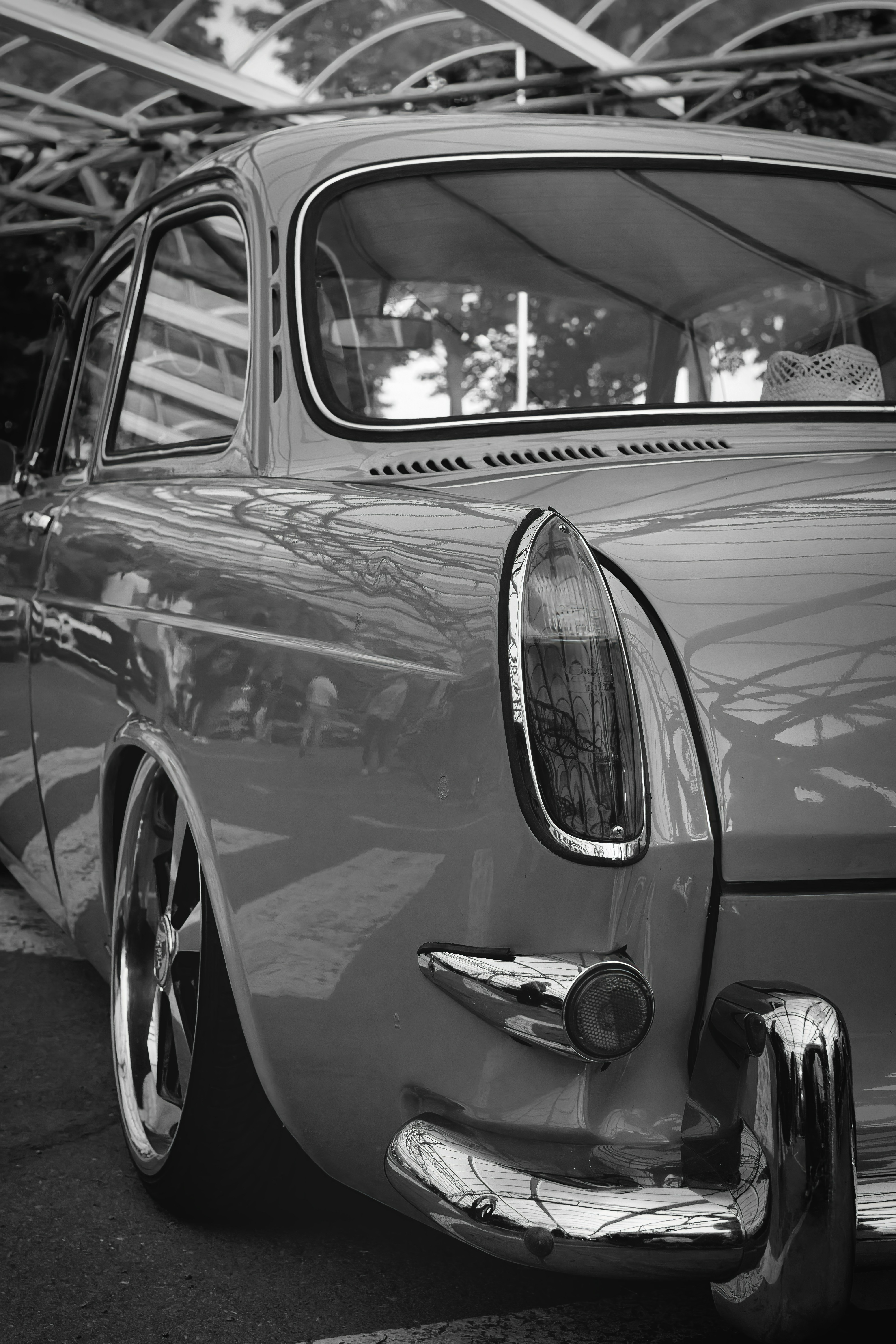 A vintage car captured in black and white, showcasing curved chrome details and reflective bodywork in a tranquil outdoor setting. This is a photographic study of light, texture, and retro design.