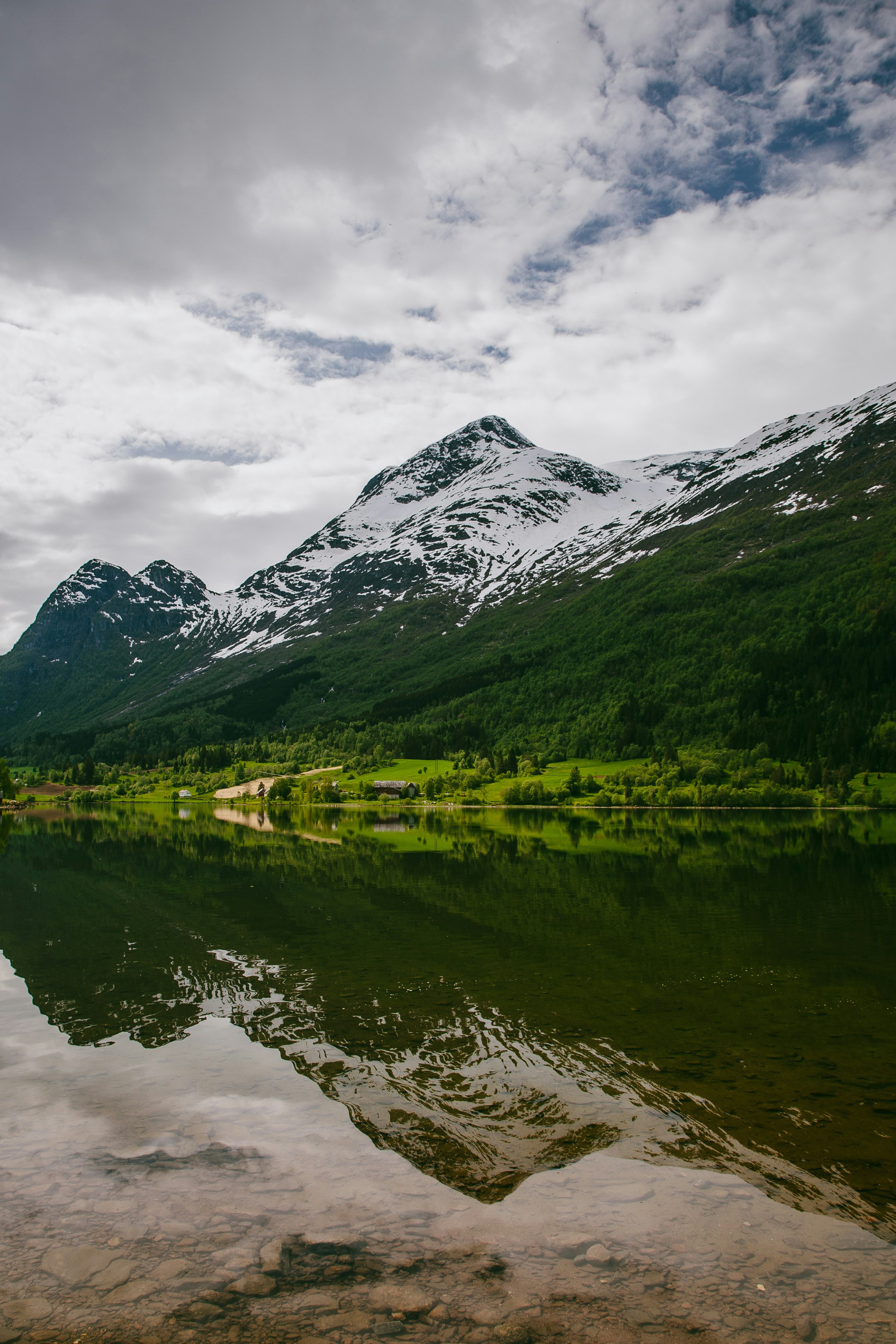 Snow-dusted mountains rise over a tranquil green valley and mirror themselves in a glassy lake.