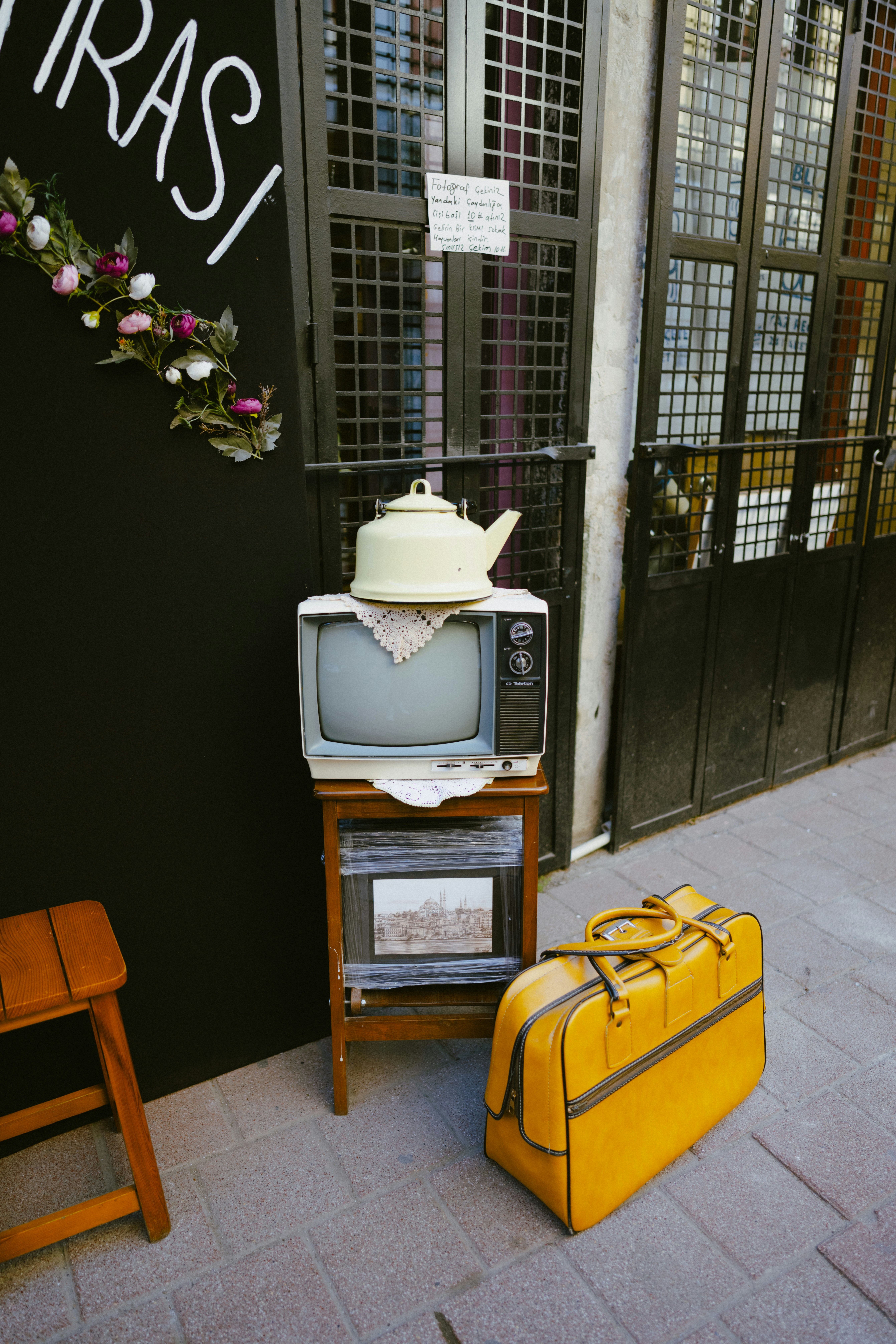 Vintage Corner: A Teapot, TV, and Suitcase Stand Guard on a City Sidewalk