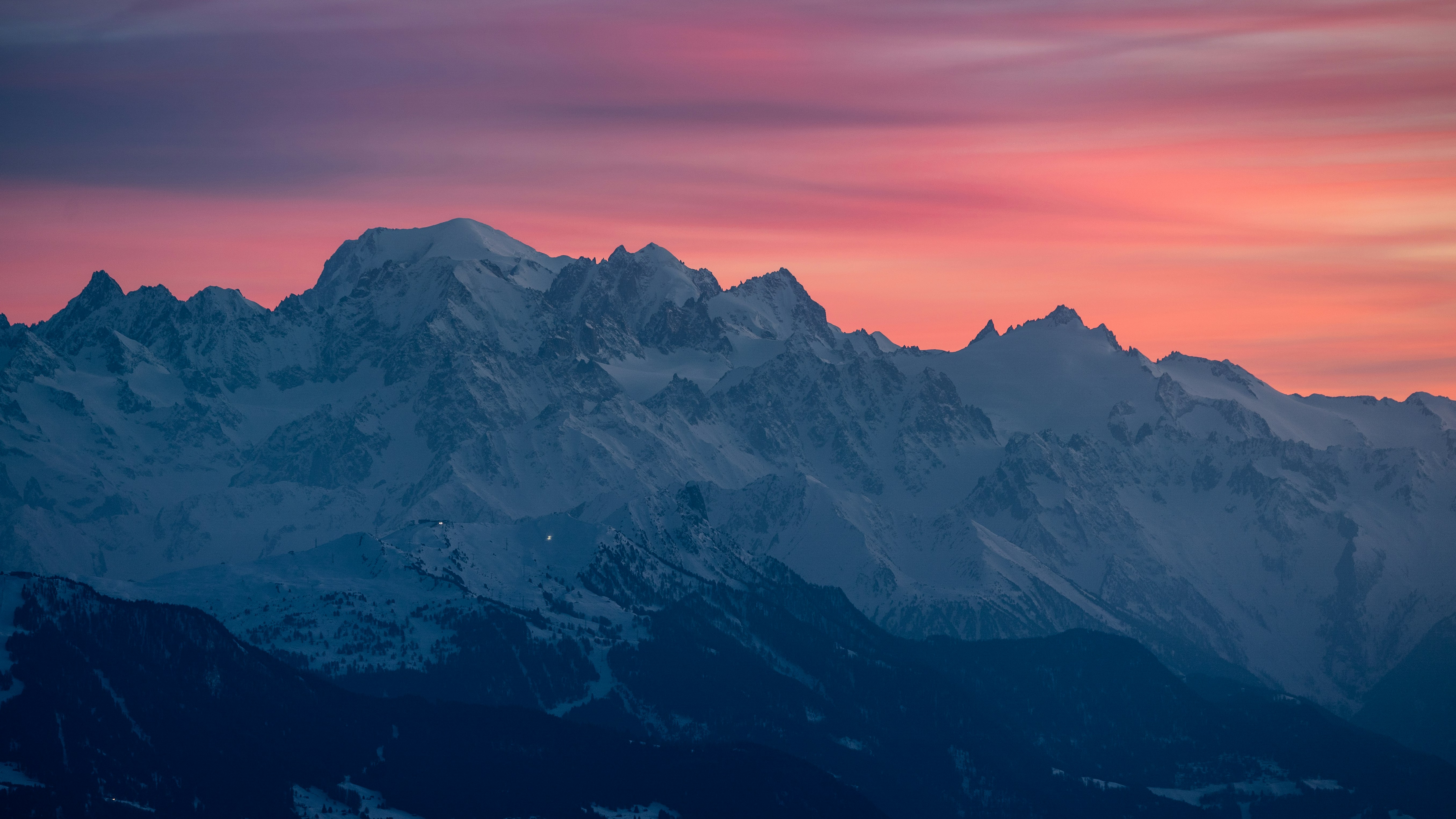 Snow-capped mountains under a pink and blue dawn sky, with subtle atmospheric haze over the range.