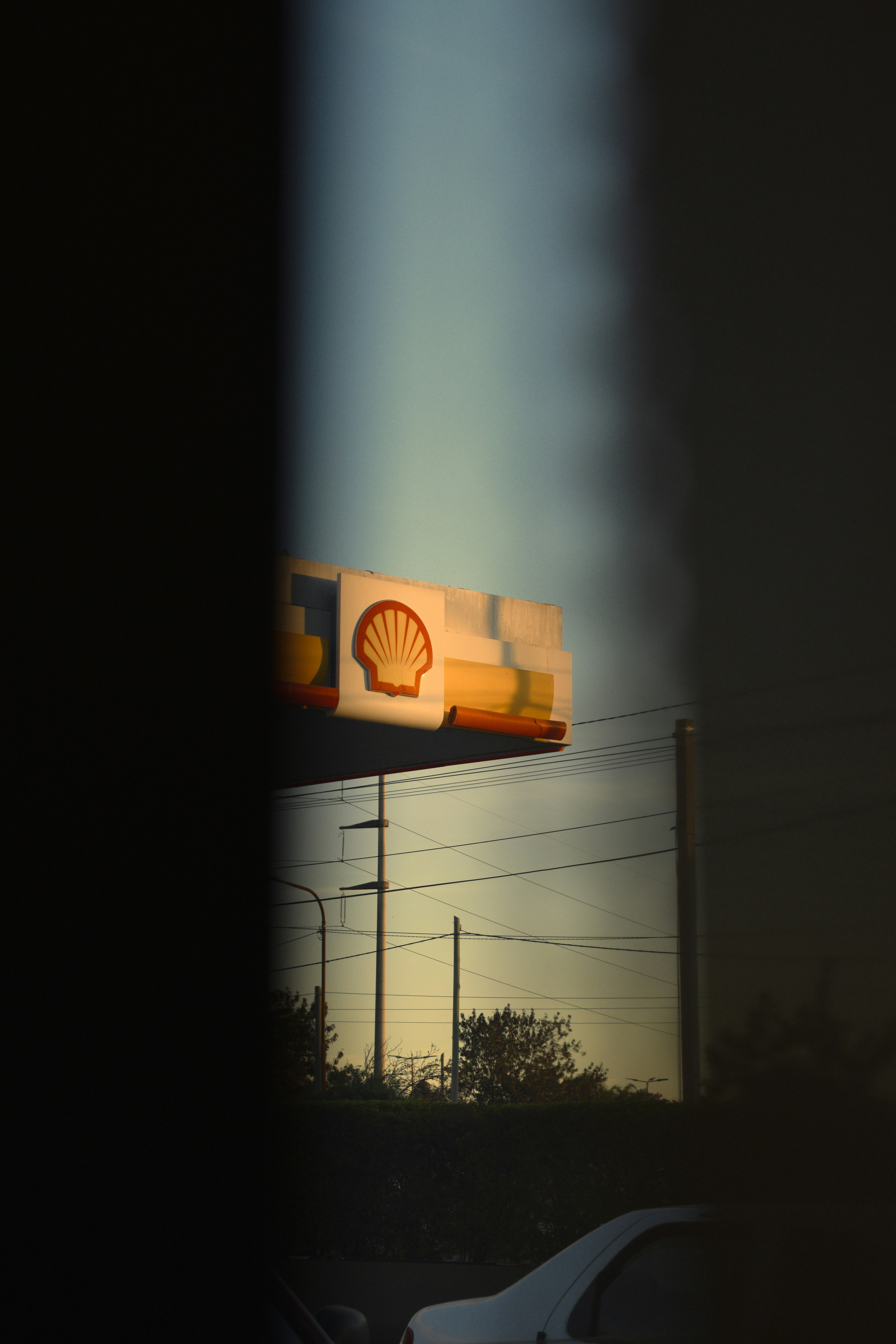 Shell logo peeking from a vertical shadowed frame over a distant gas station sign