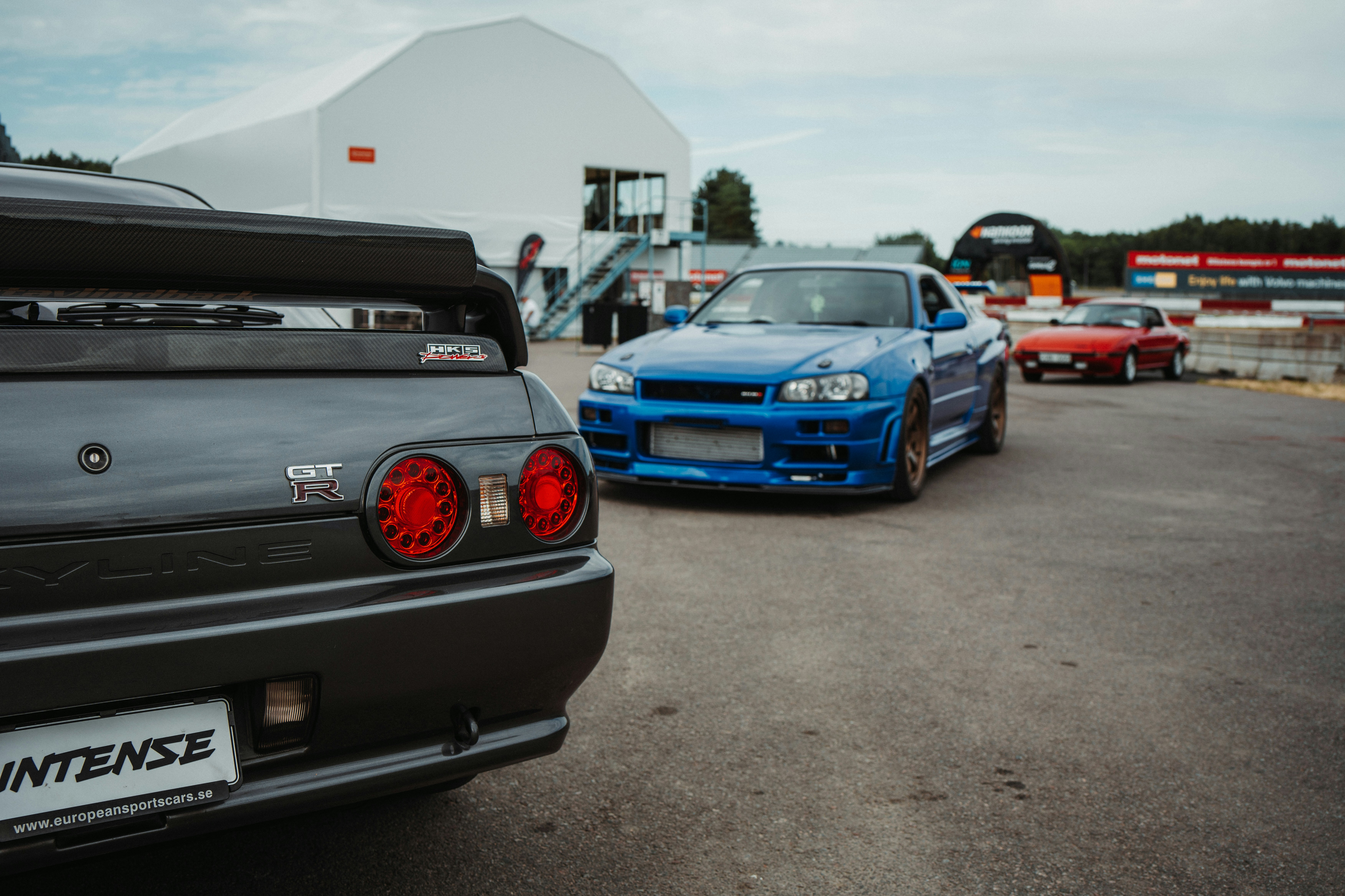 Rear-View Lineup: A Street of Tuned Sedans and a Blue Challenger Rounding the Corner