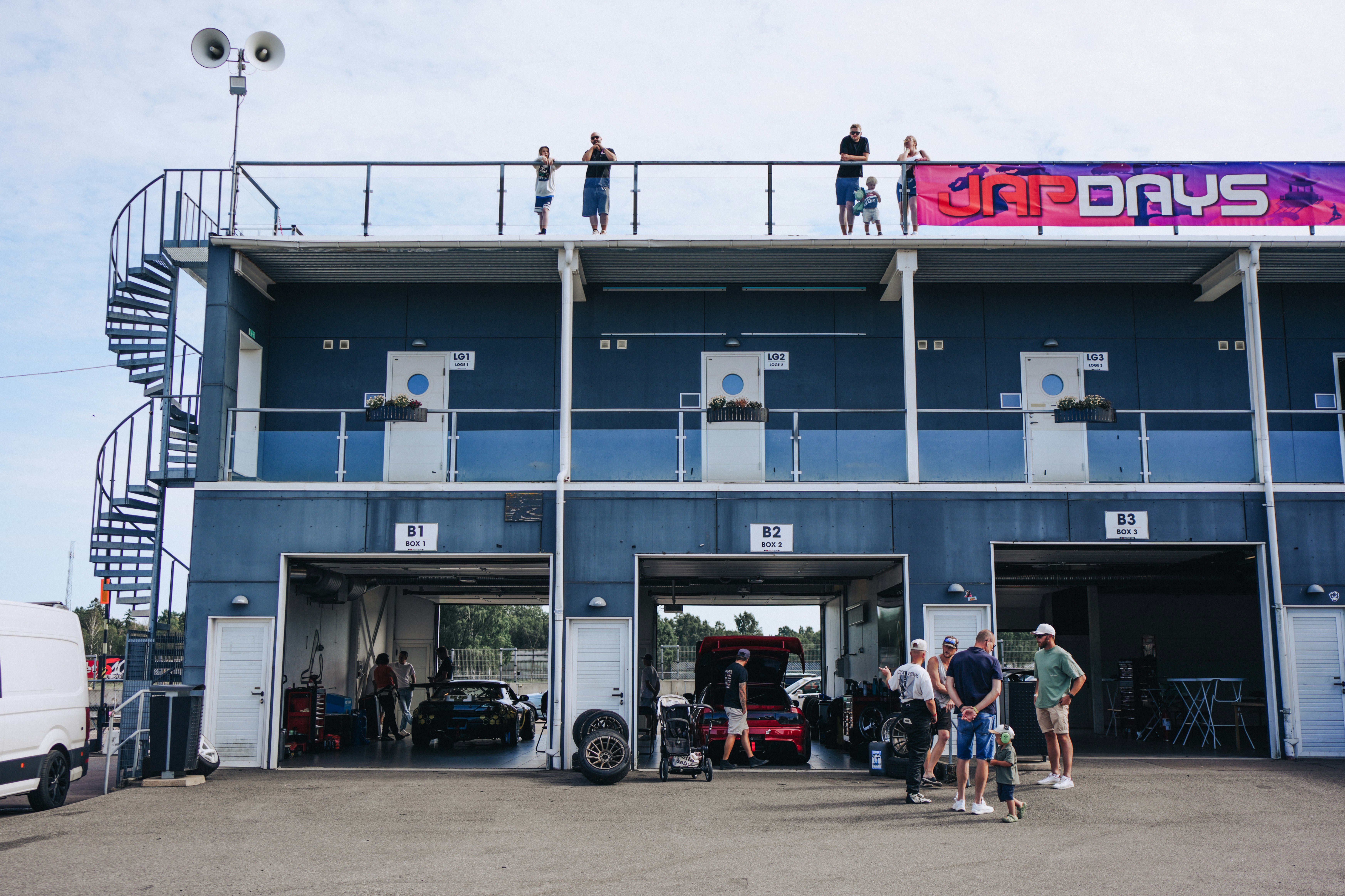 Pit Lane Panorama: A Blue Grandstand Breathing with People and Cars