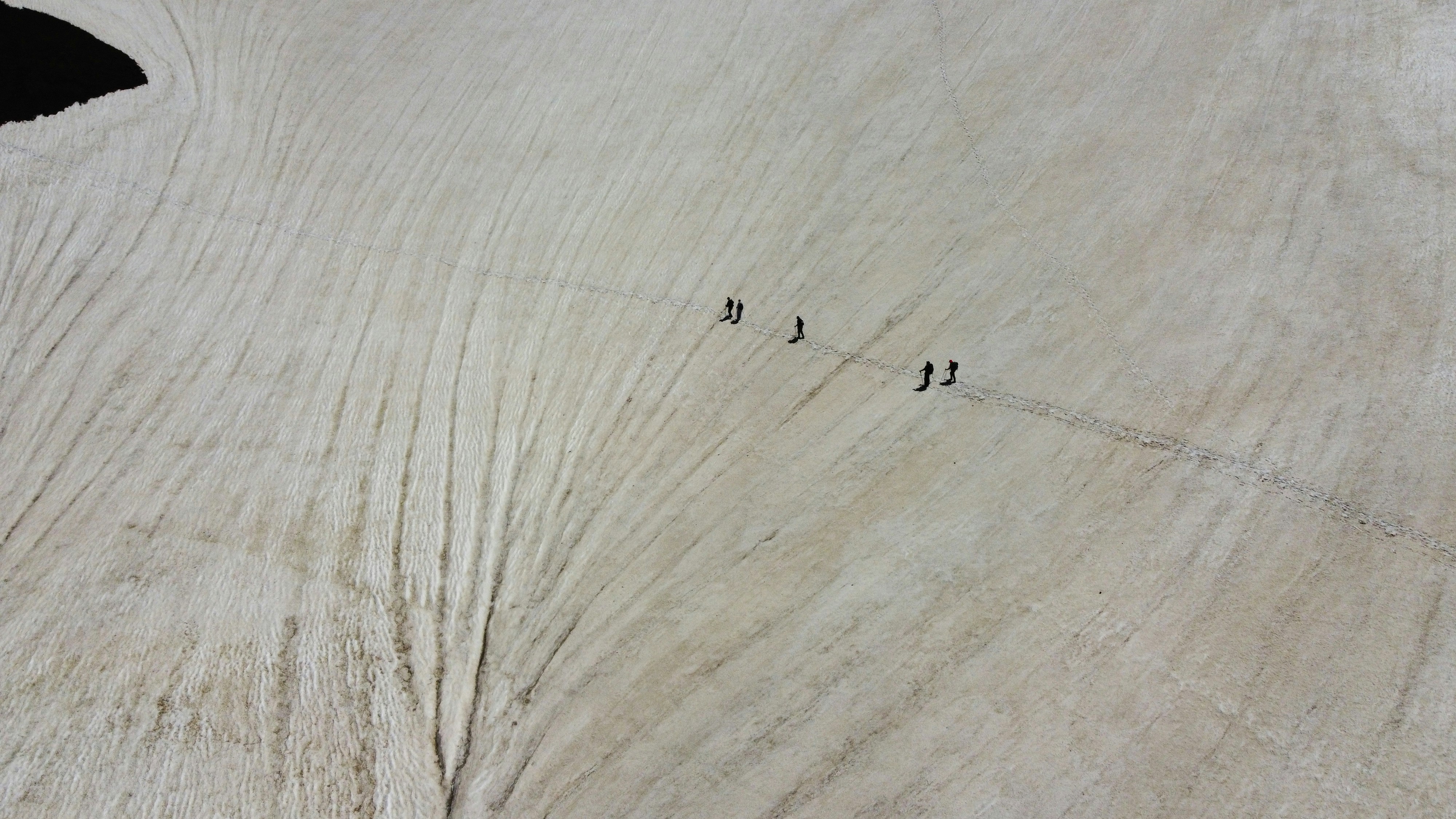 Dust trail and distant travelers across wind-sculpted desert dunes