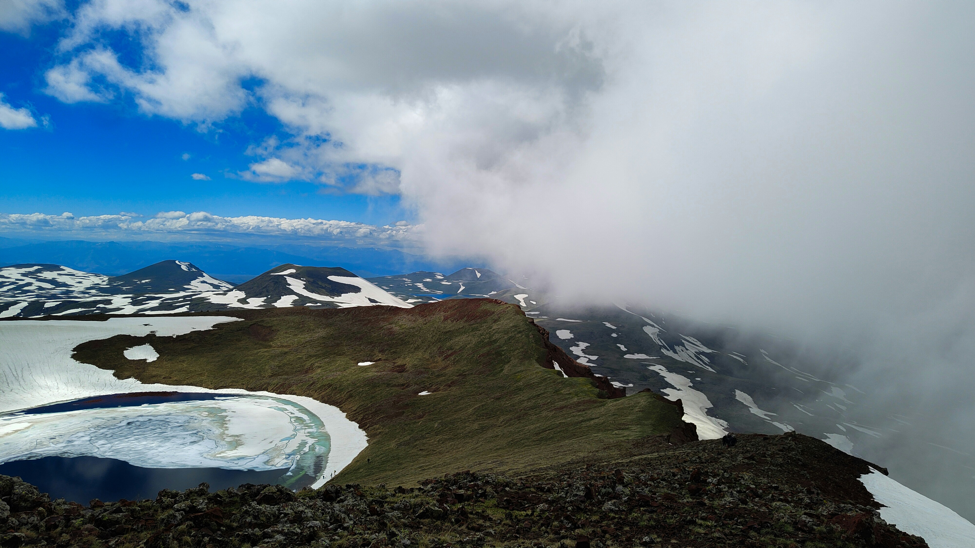 Snowy ridge under a break in the clouds over a glacial pool