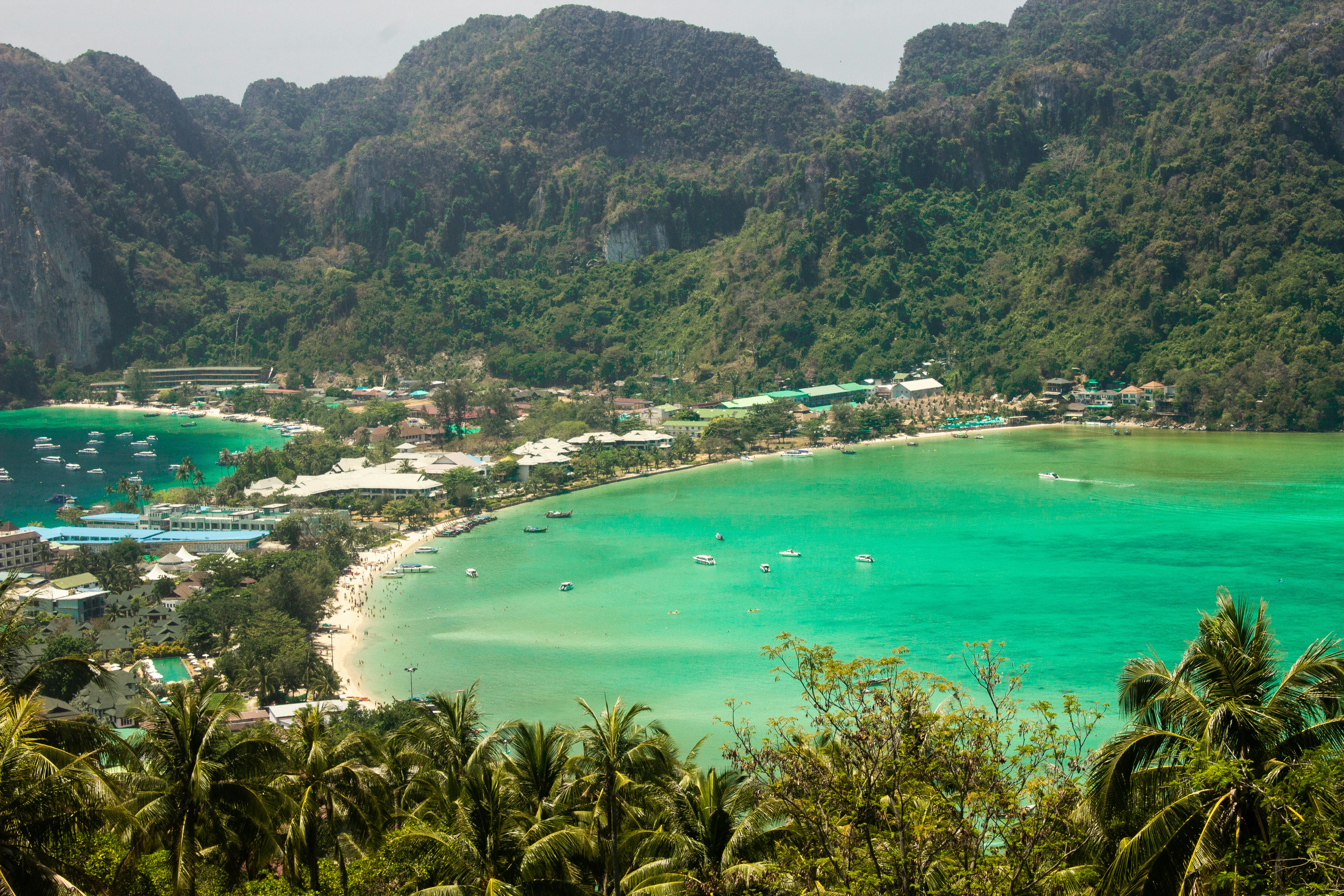 Vibrant turquoise bay fringed by palm trees and a small resort cluster along a crescent beach.