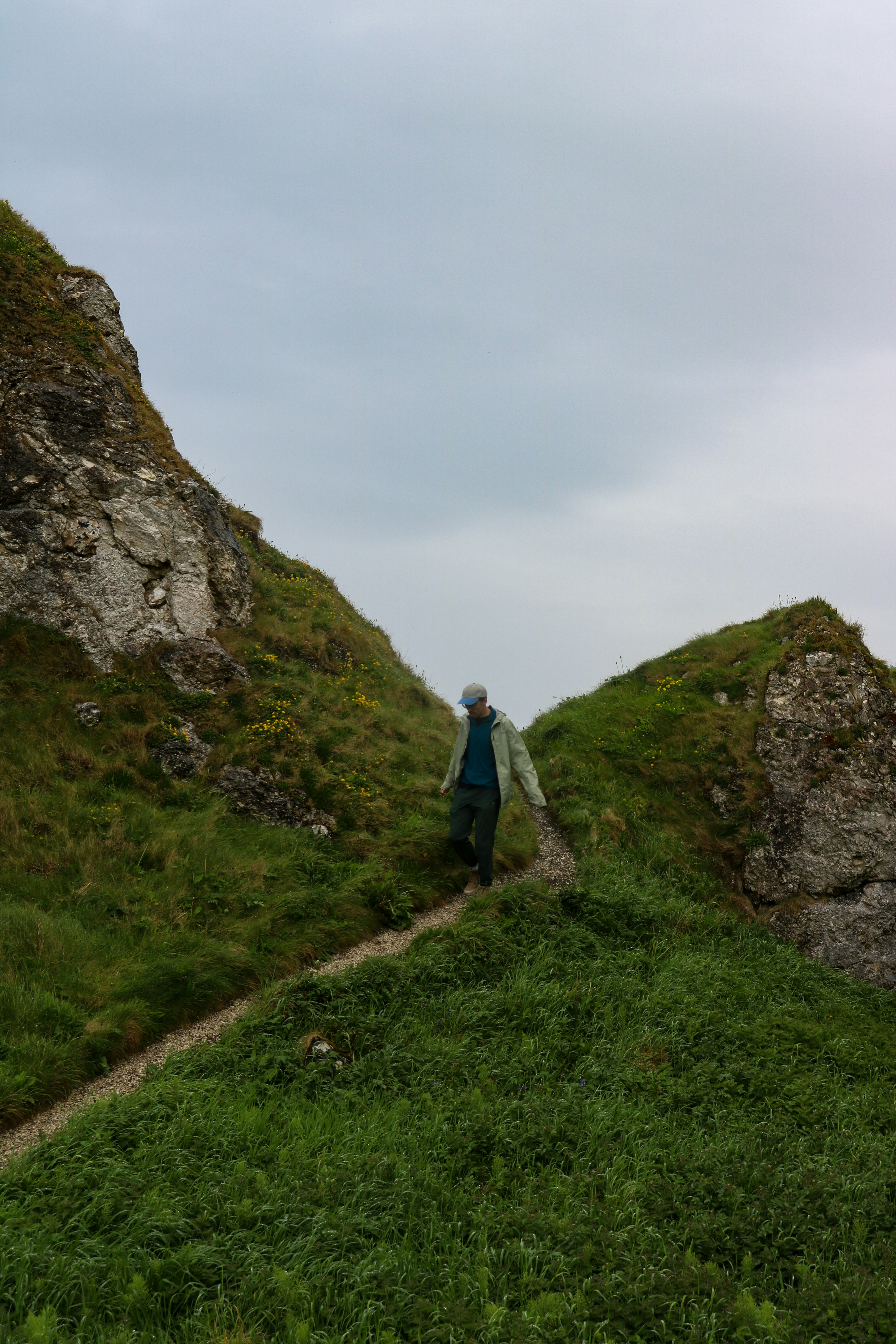 Trail through emerald cliffs: a lone hiker ascending a grassy path