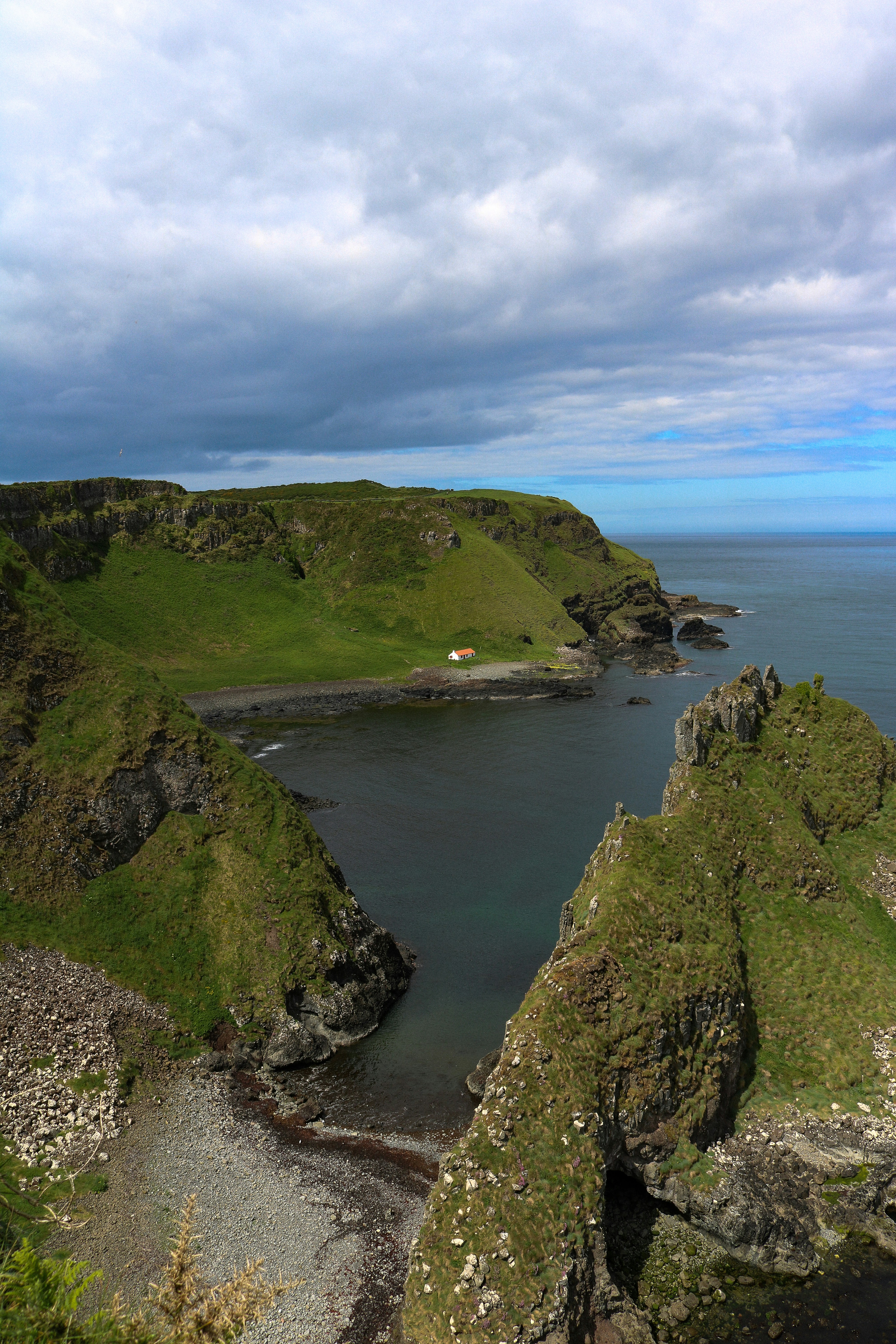 Green cliffs and a lone cottage by the seaward inlet