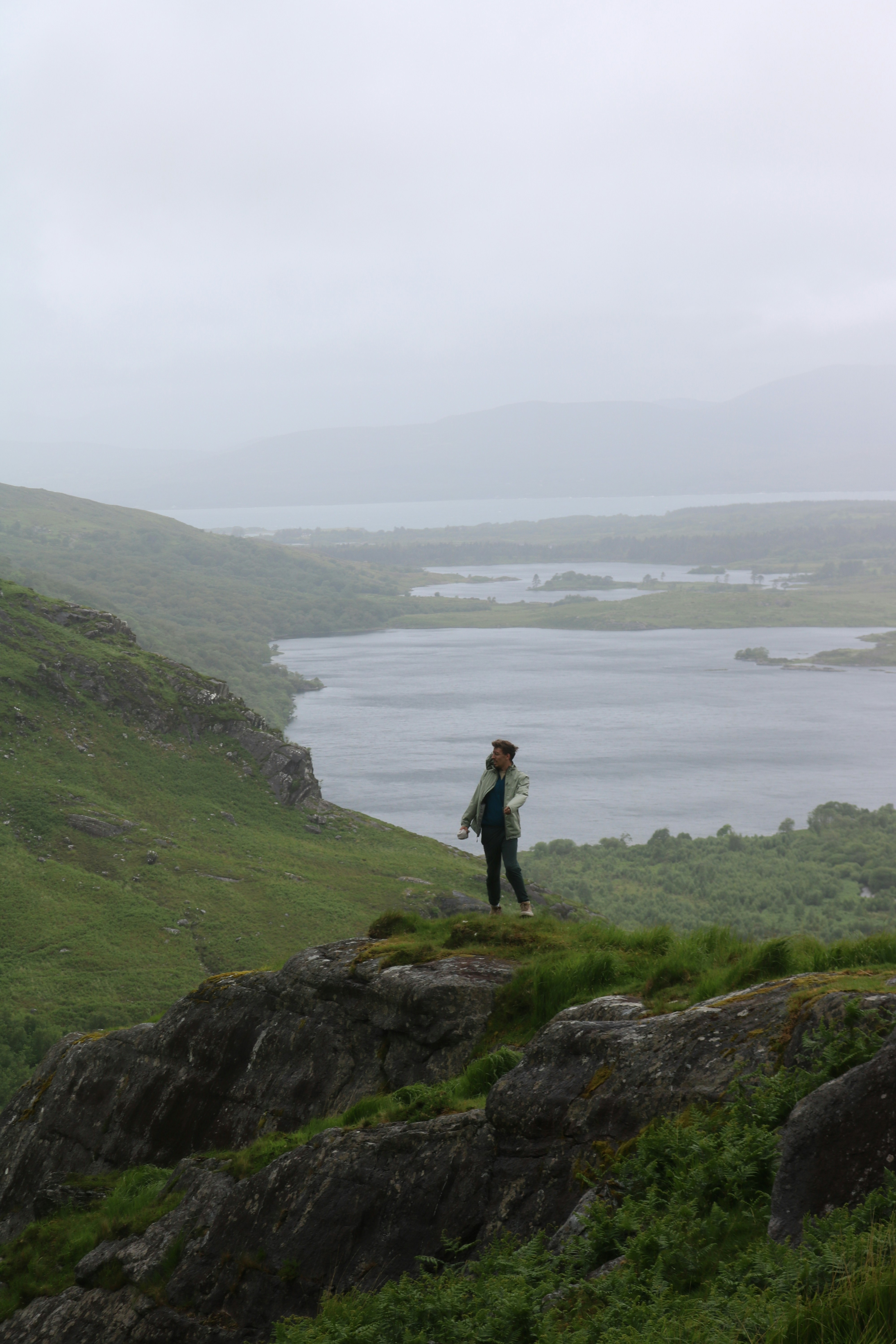 Lonely Outcrop: A Figure Amid Mist over Verdant Valleys