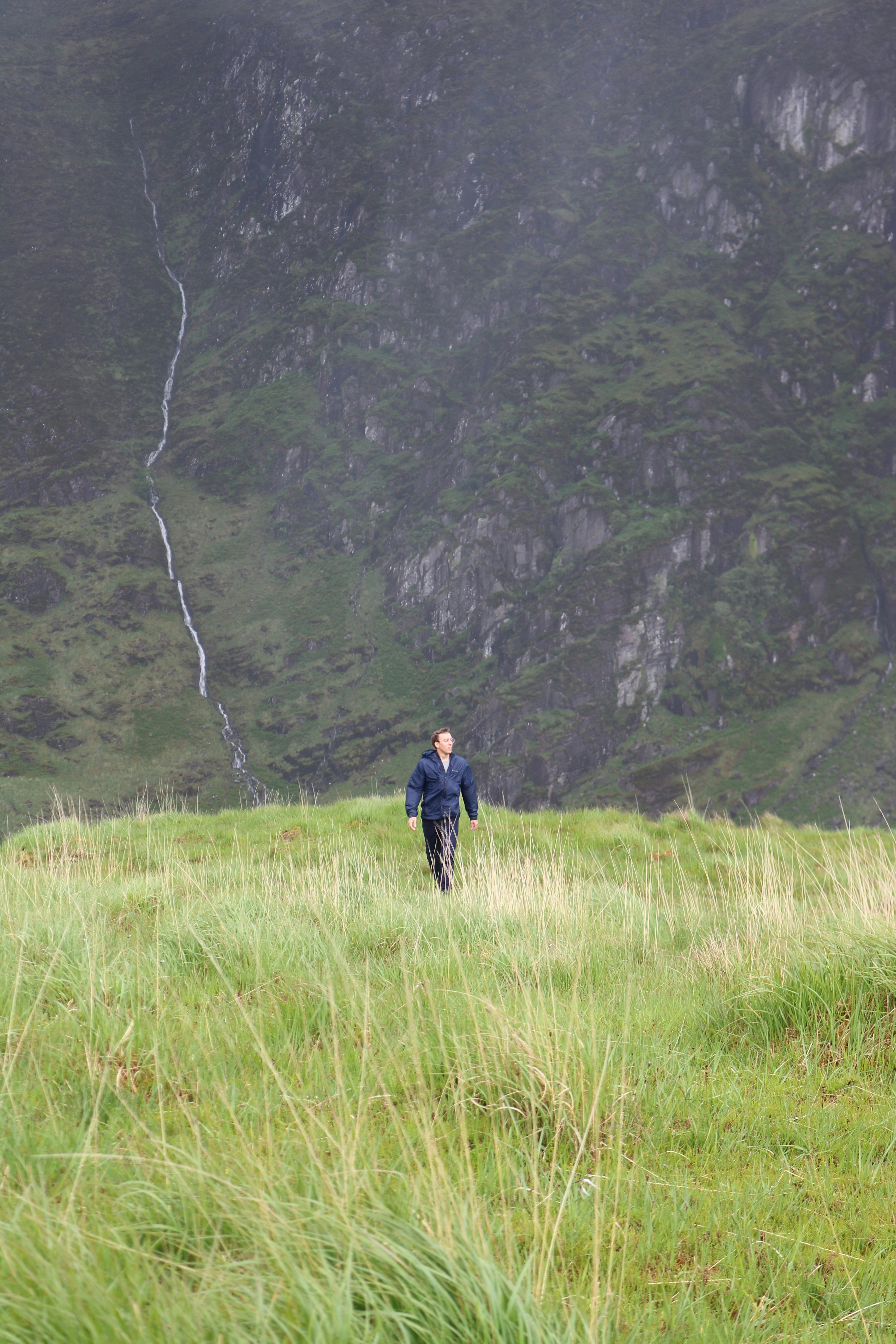  lone traveler in a windswept valley before a towering waterfall cliff