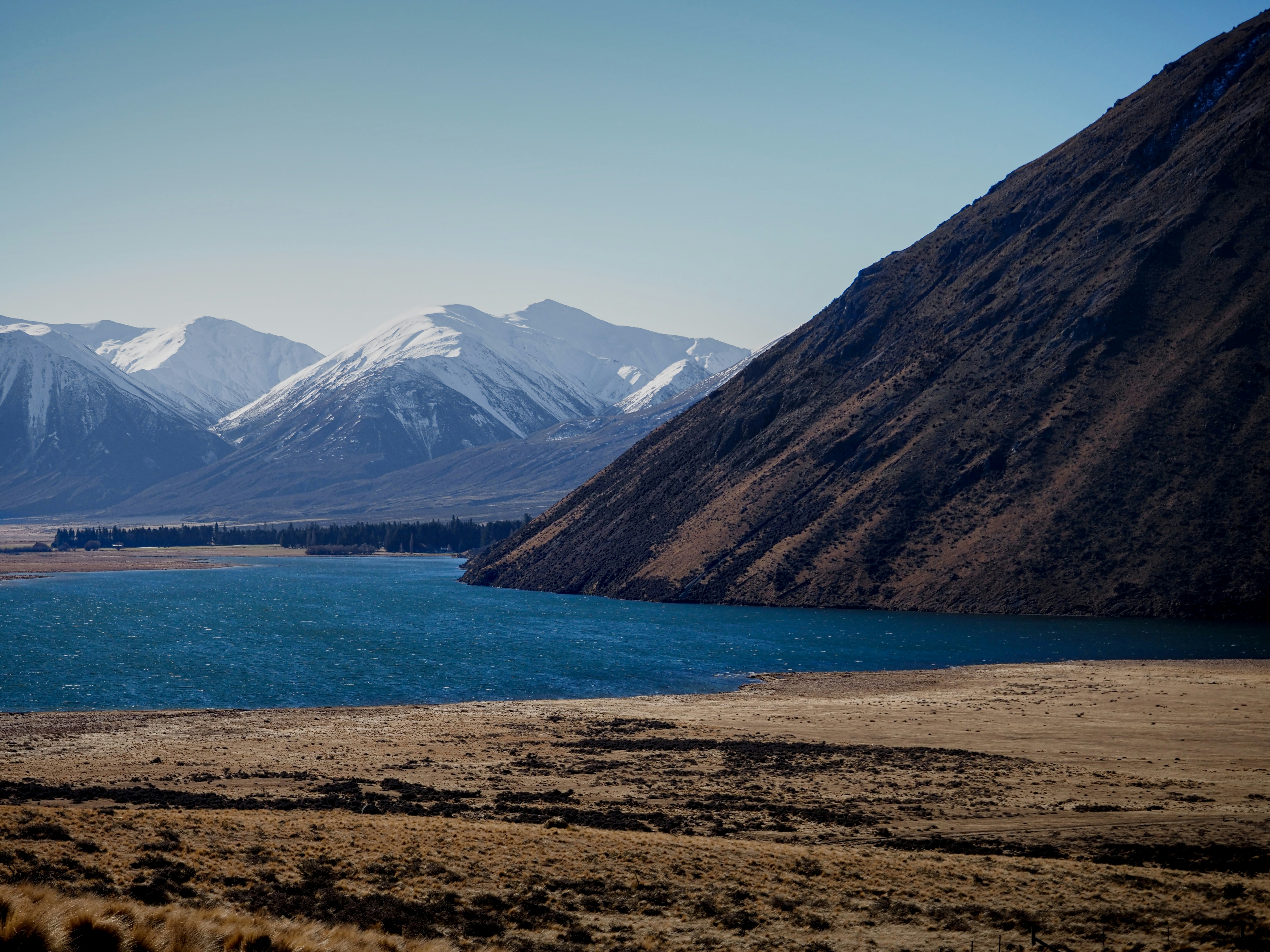 Snow-dusted peaks meet a cobalt lake by a shaded mountain slope