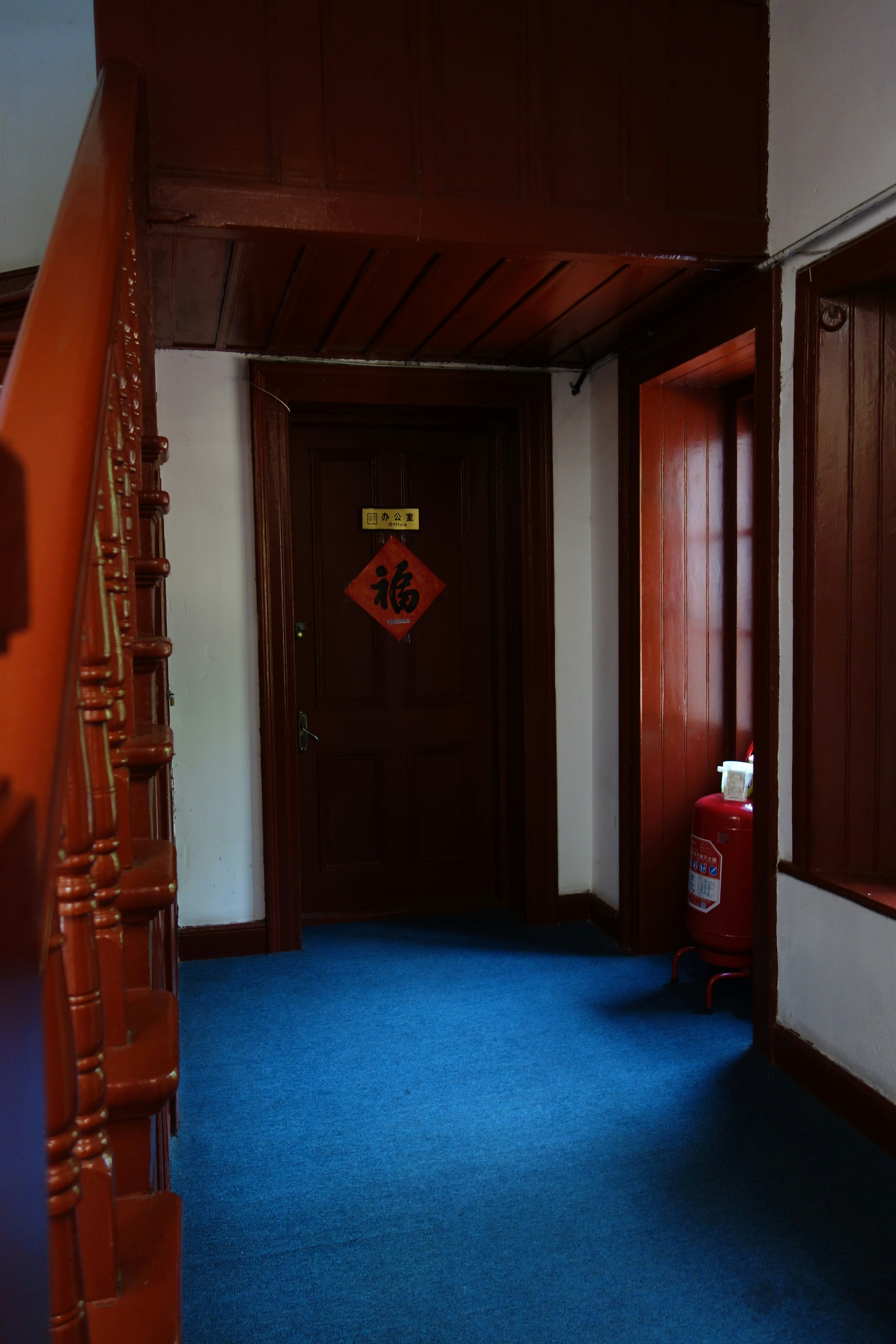 Blue carpeted hallway with wooden door and red fire extinguisher.