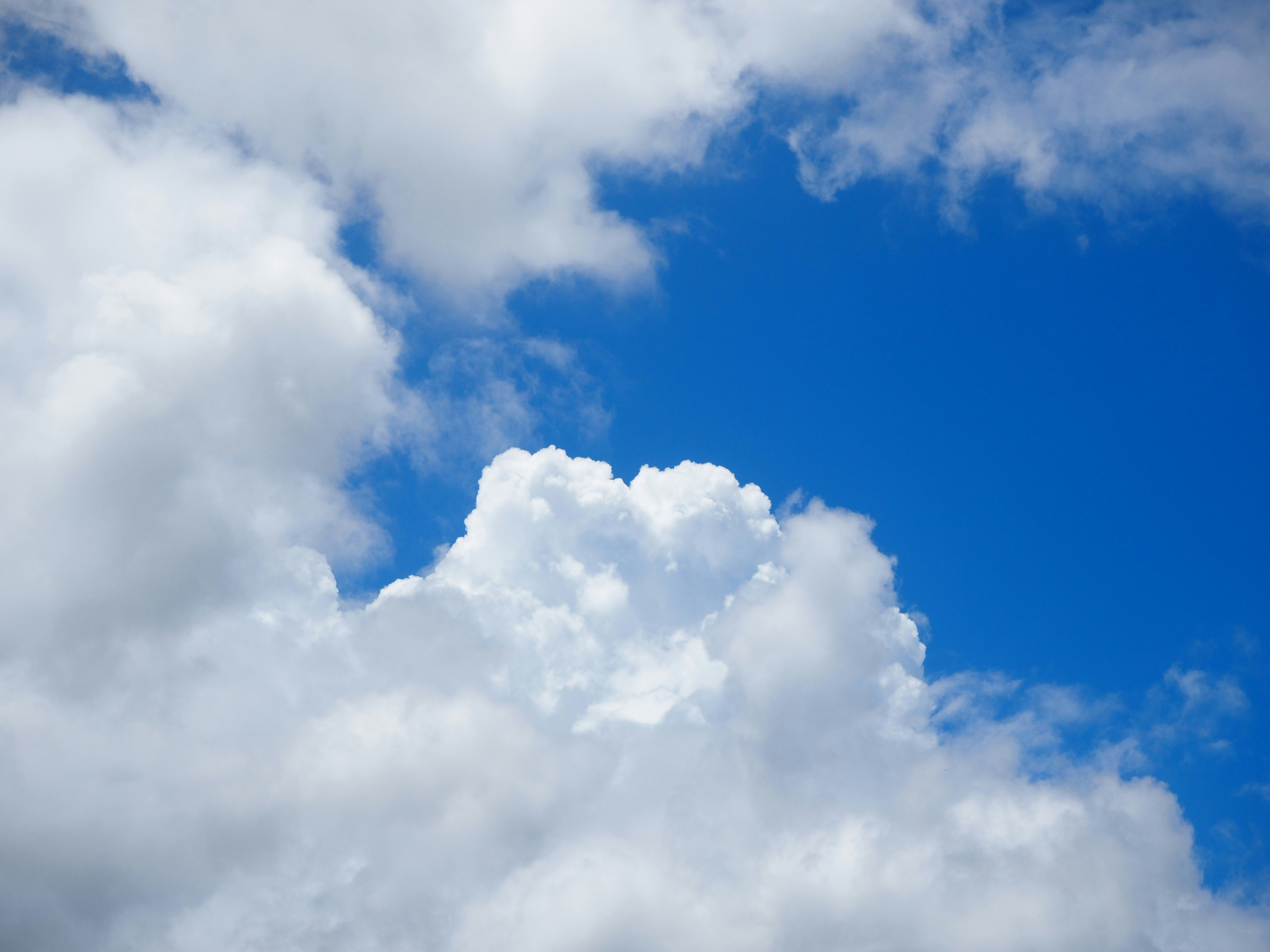 Bright cumulus clouds drift across a vivid blue sky with soft, glowing edges, conveying a serene, open-air atmosphere.