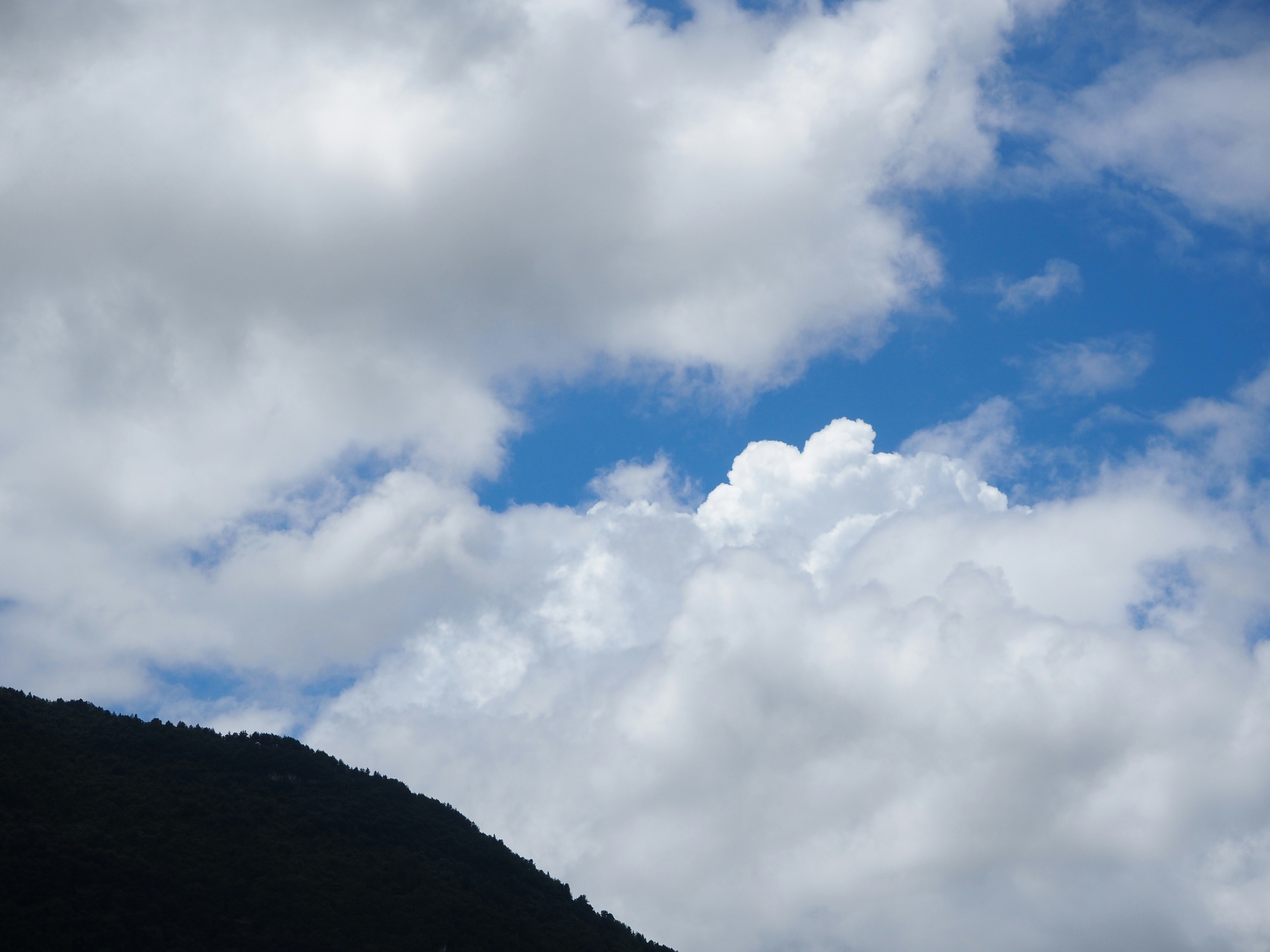 A wide landscape of a ridge under a bright blue sky with fluffy white clouds; the scene emphasizes natural light and expansive atmosphere. This is a photographic capture of the sky and terrain, not a painting or illustration.