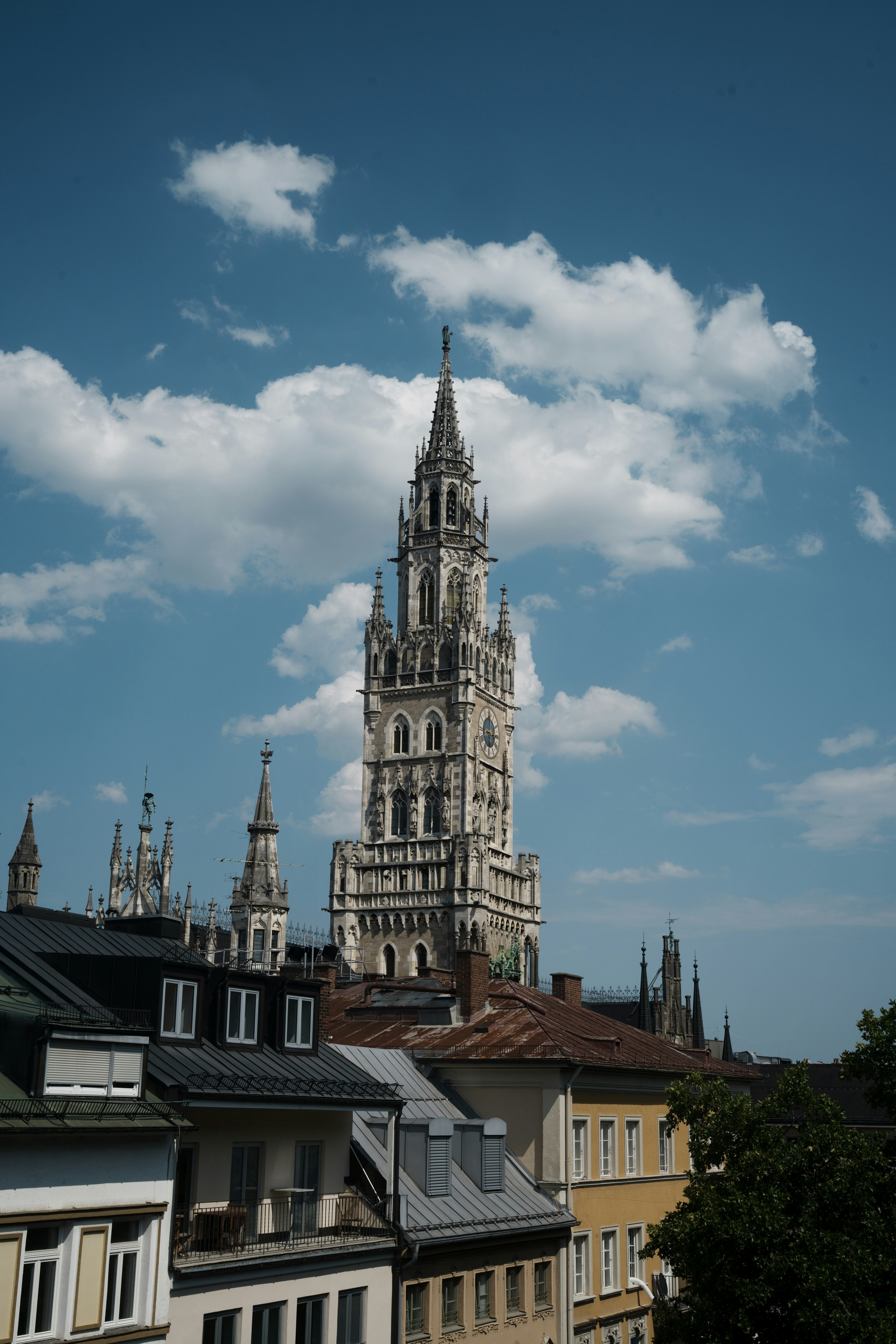 Tall cathedral spire rising over lower European rooftops against a bright sky.