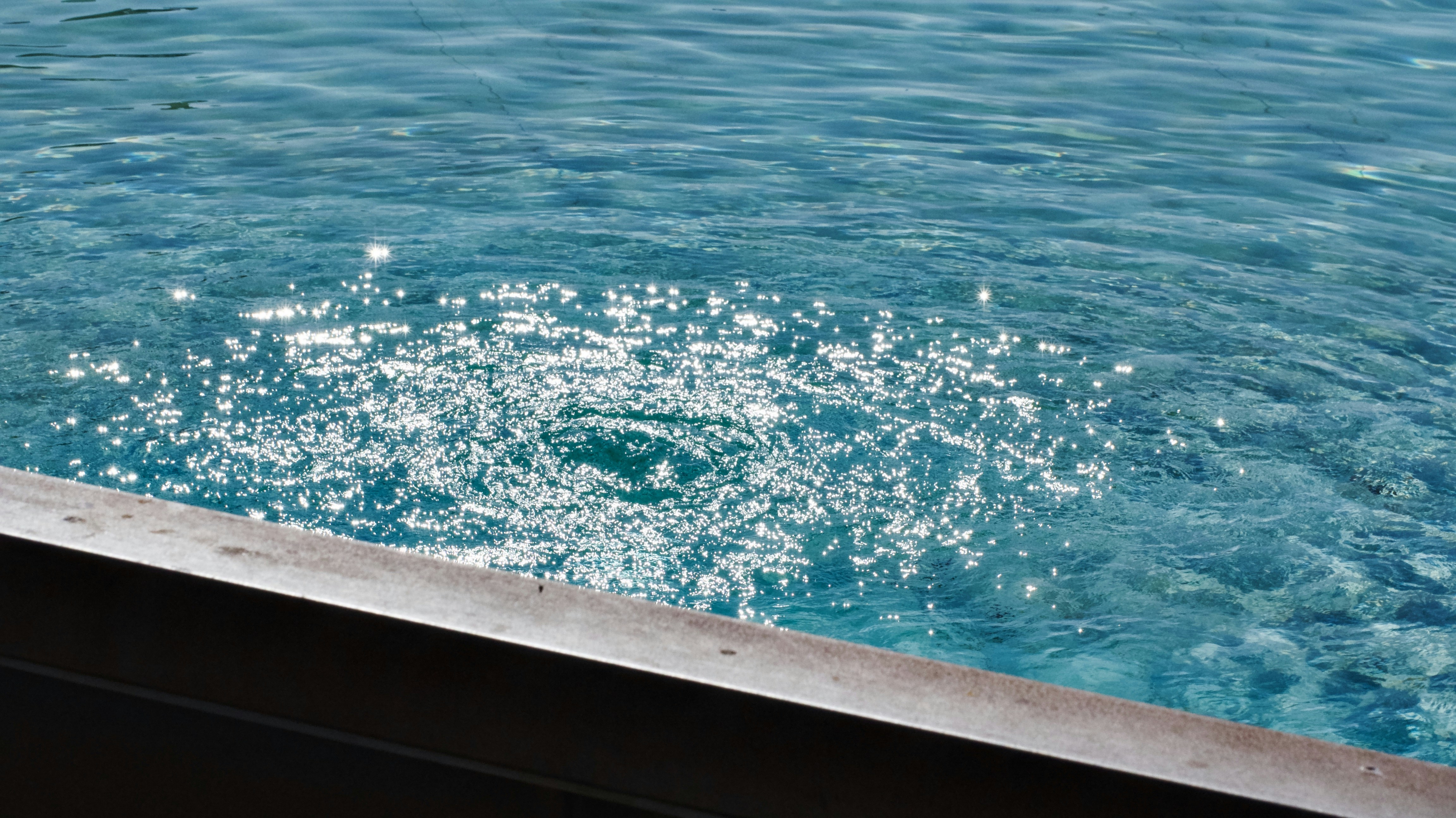 Sunlit Ripples Over Clear Waters by a Dockside Barrier