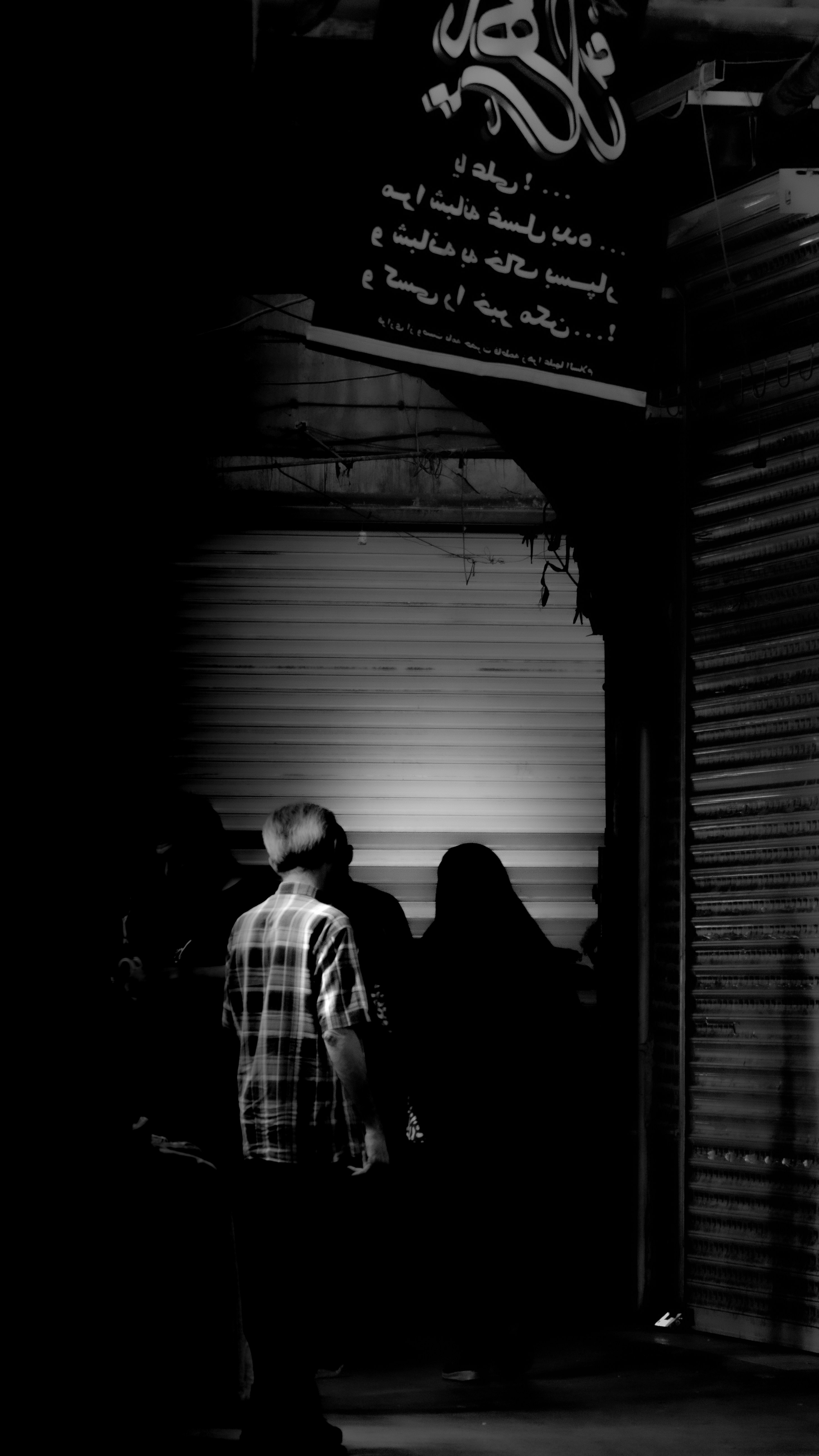 Shadowed Entrance: A Stranger’s Pause Beneath a Glimmering Shutter