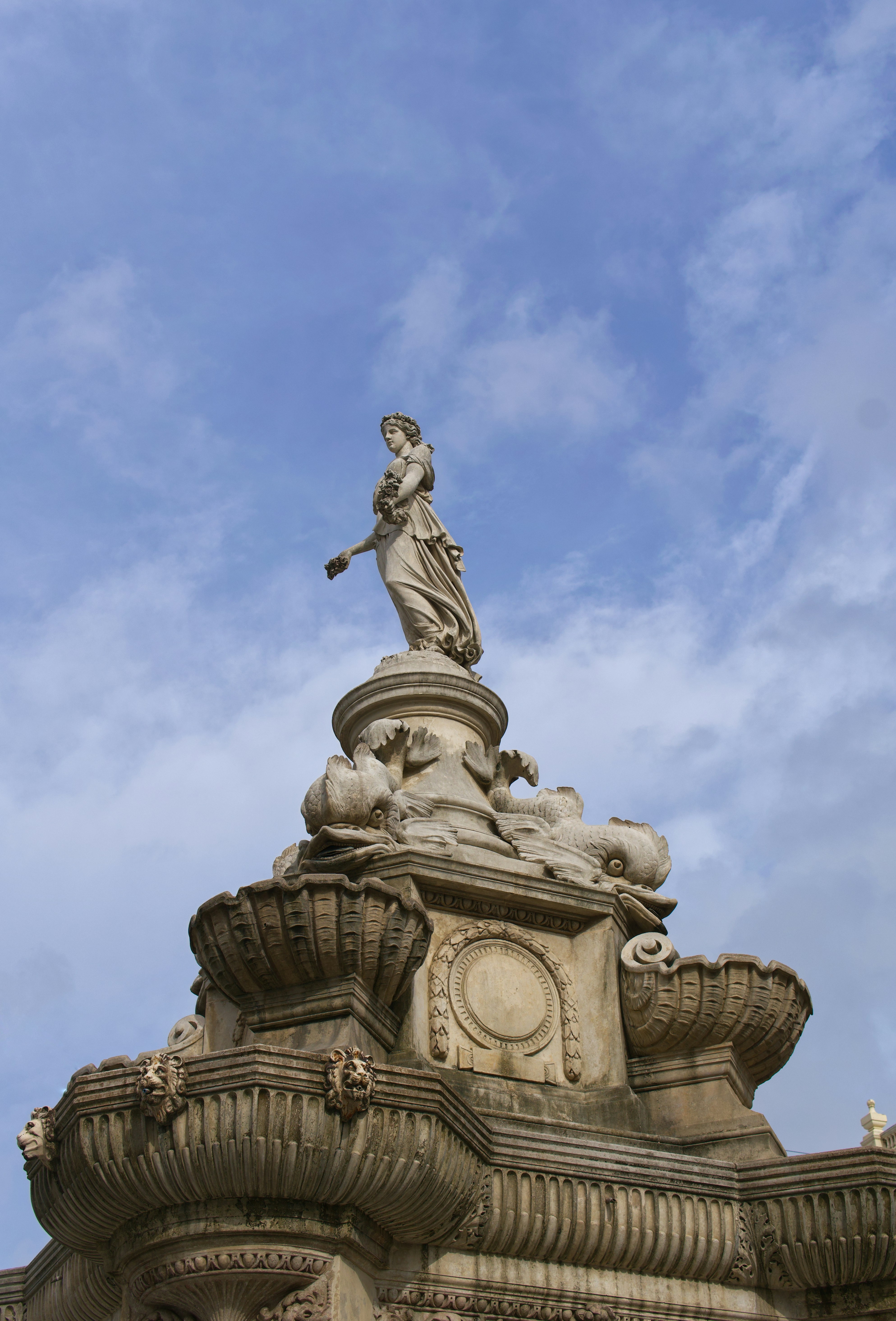 Ornate stone statue atop an elaborately carved pedestal against a blue sky, highlighting sculptural details of the monument.