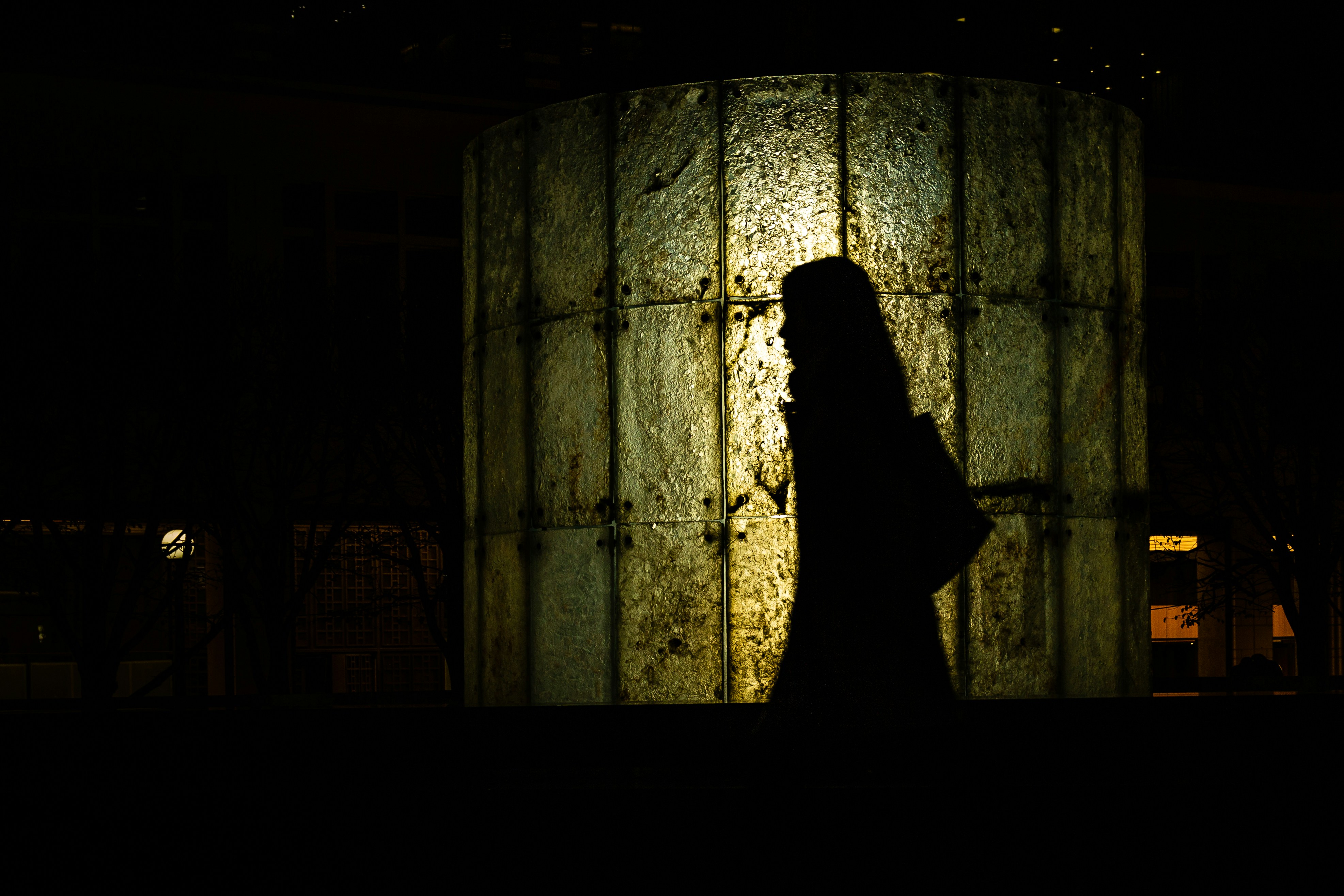 Silhouette in the Night: A Quiet Walk Past a Glowing Cylinder