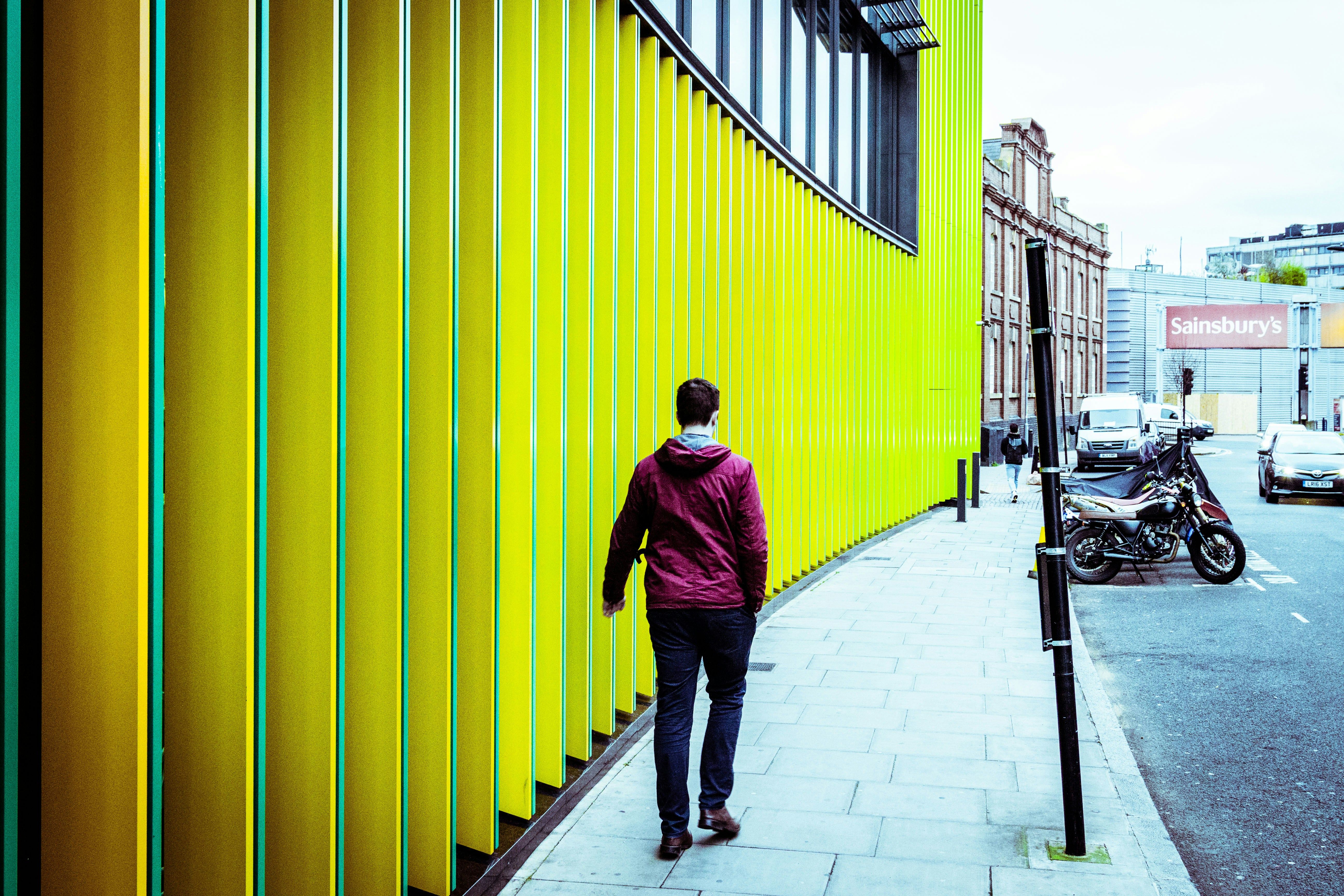 Man in maroon jacket walks along a vivid yellow wall-lined street