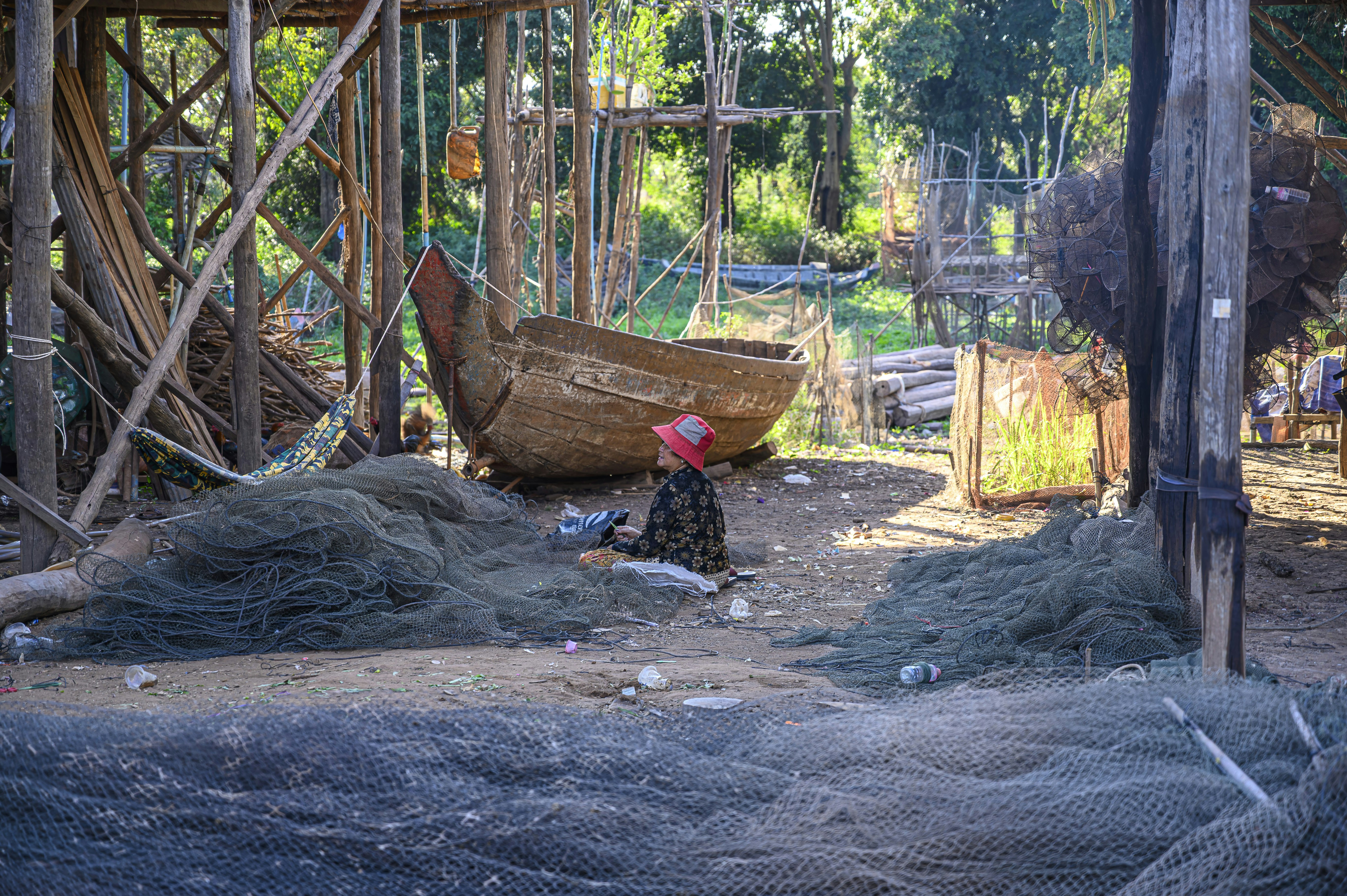 Worker in a coastal yard trims nets beneath weathered structures