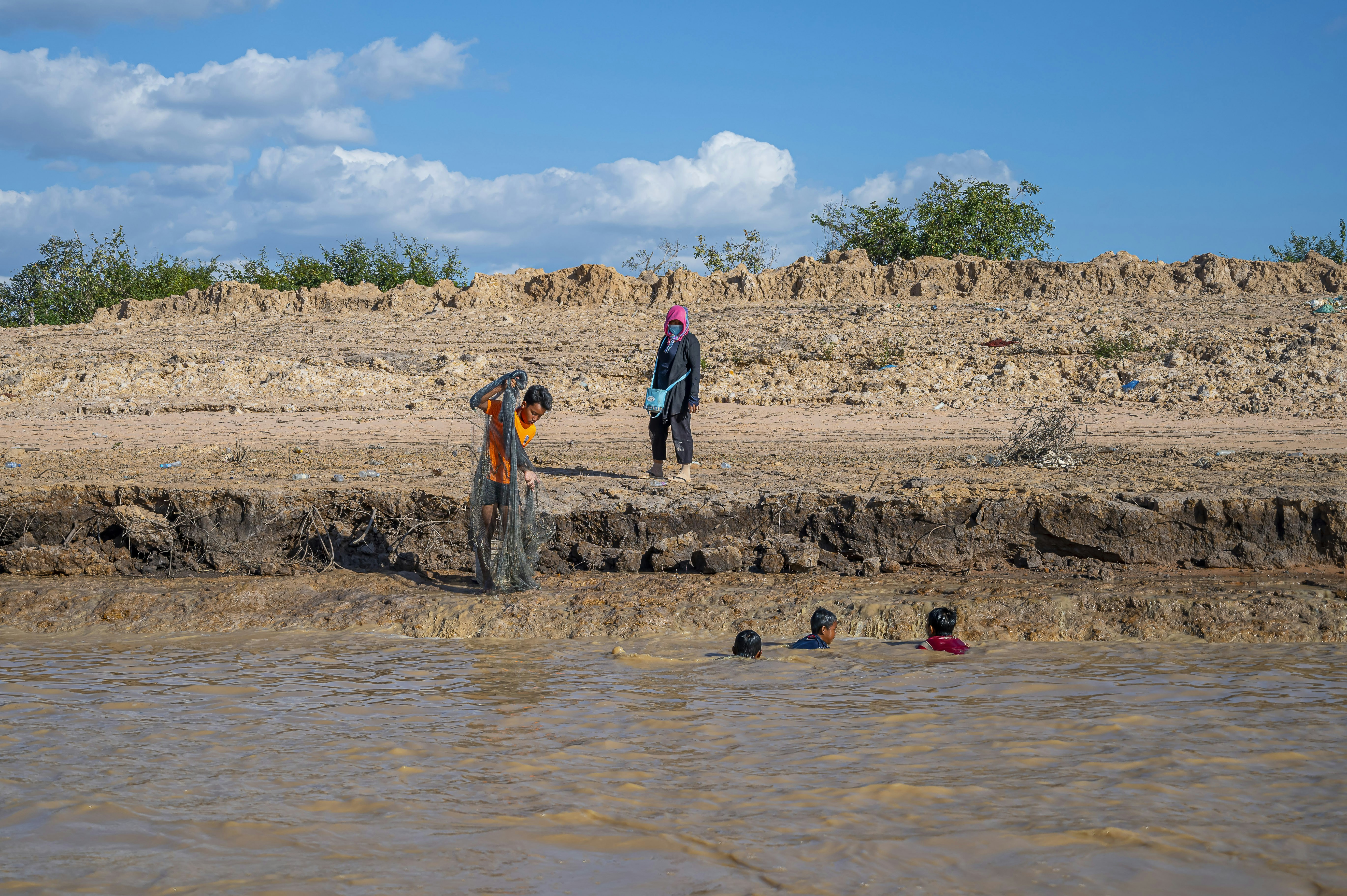 Crossing at the Riverbank: Faces and Distant Camps Amid a Dry Terrain