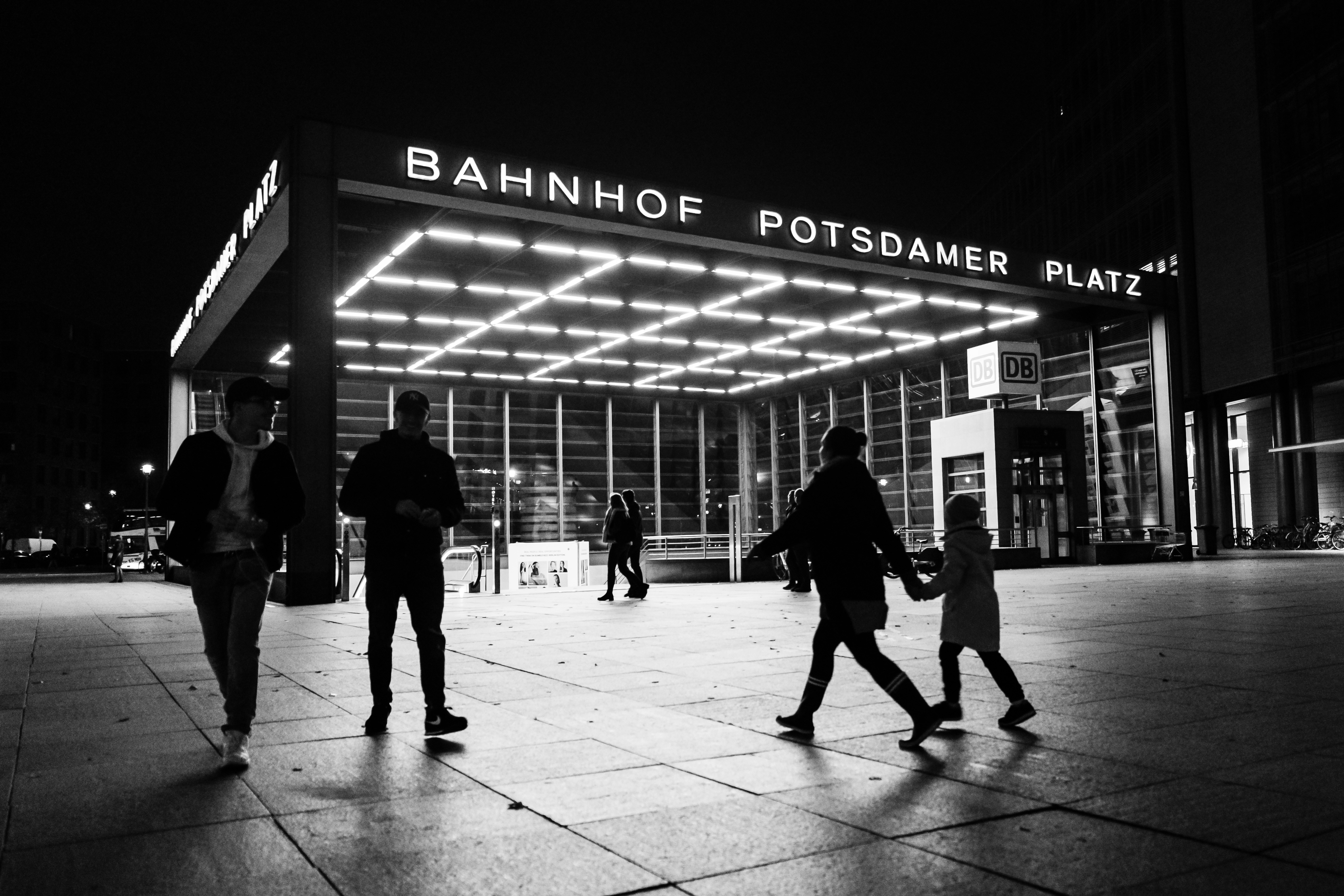 Night at Potsdamer Platz: Striding Figures Before the Illuminated Station