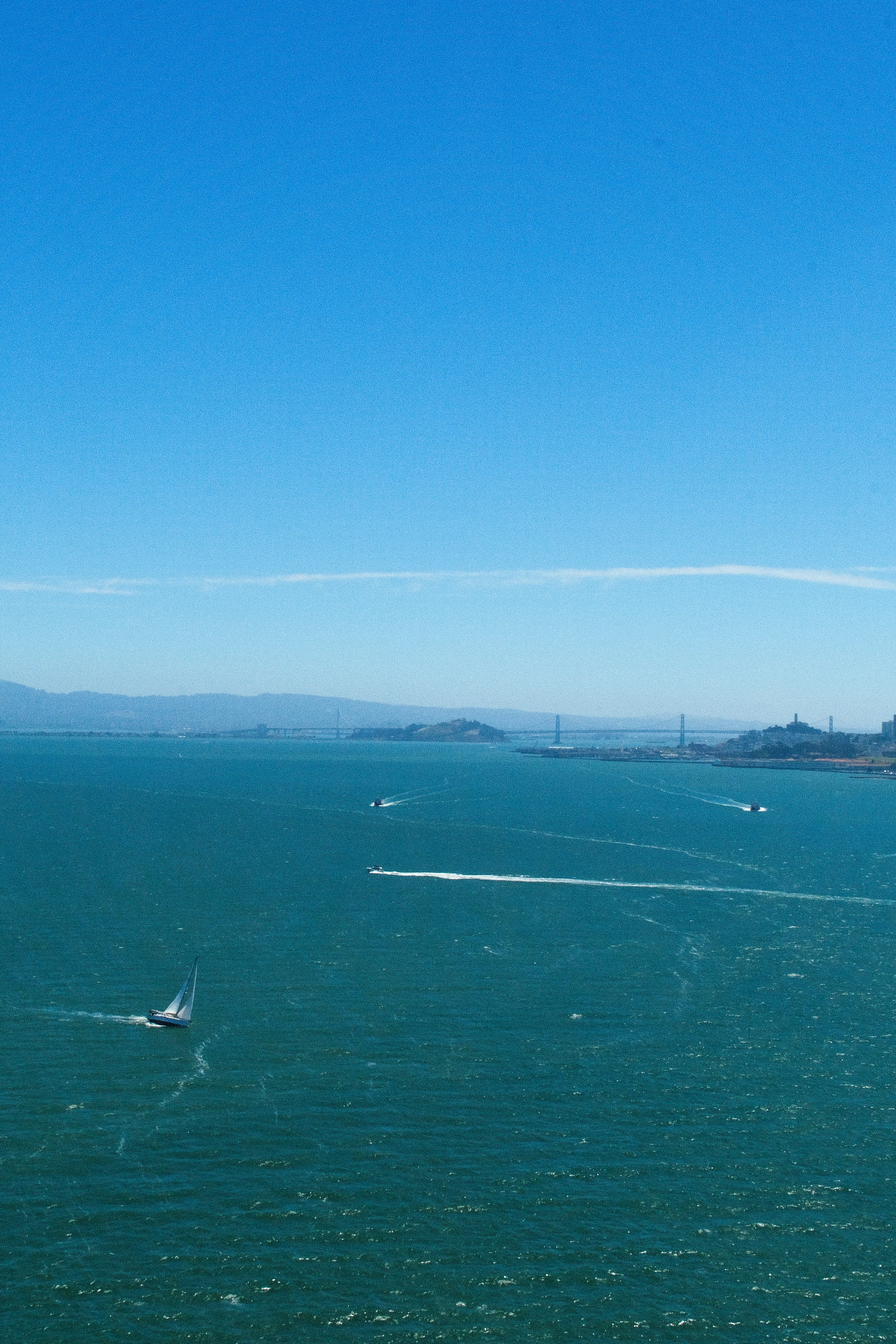 Verdant Wake: A Sailboat Tracing White Streaks Across Coastal Blue