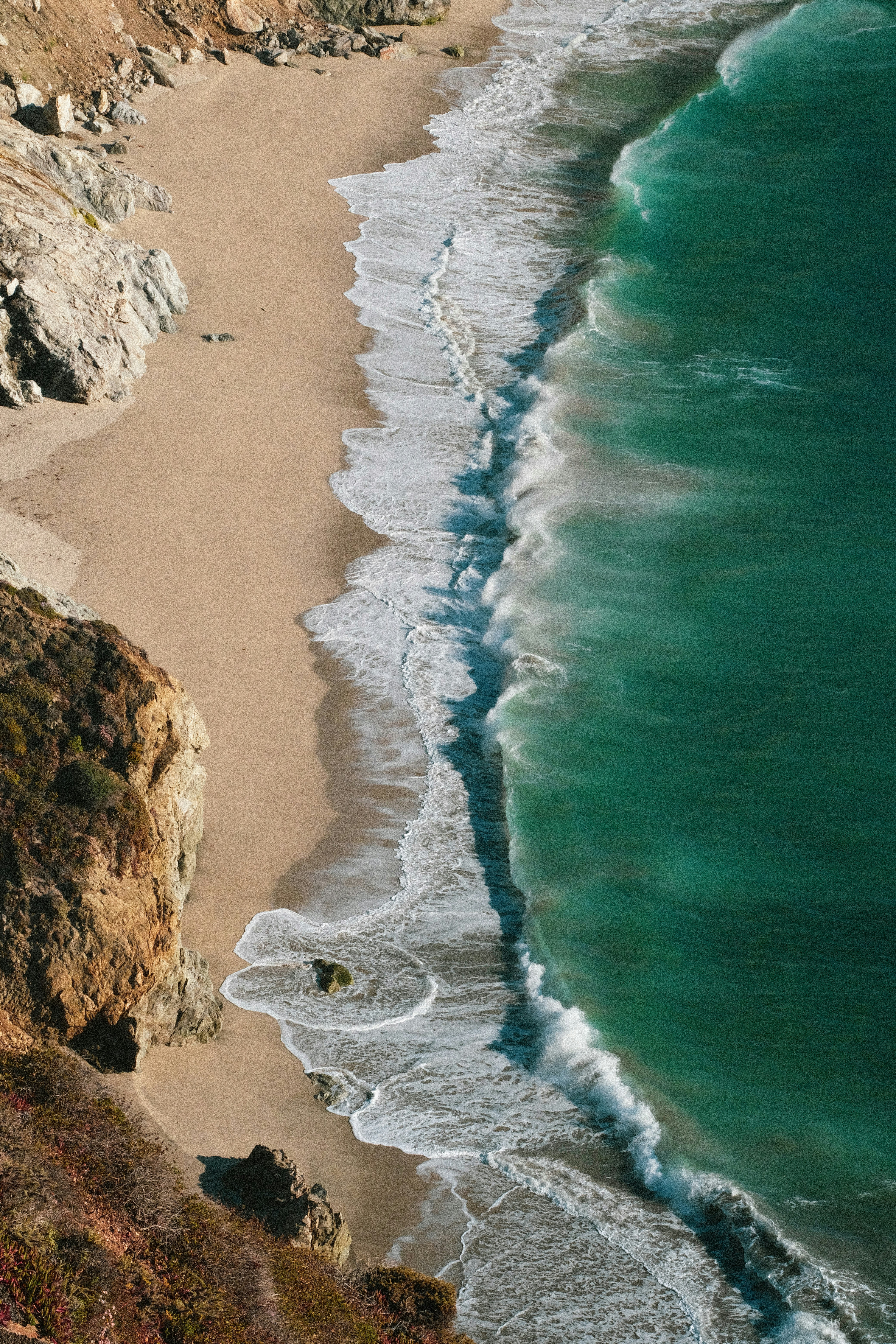 Coastal Divide: Aerial View of Sand, Cliff, and Turquoise Surf