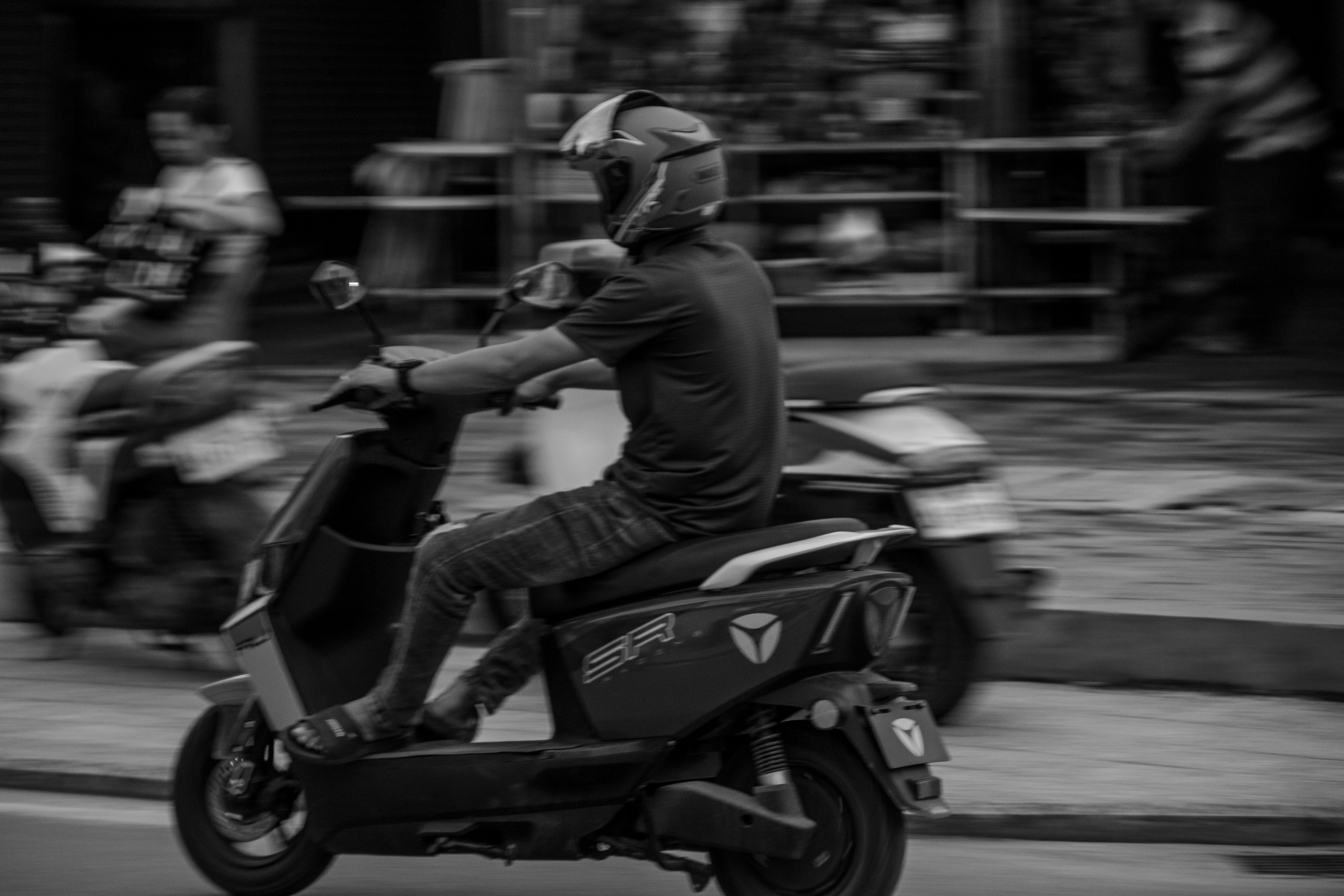 A rider on a scooter moves through an urban street, captured in motion with a shallow depth of field and motion blur, highlighting the vehicle and rider against a blurred background.