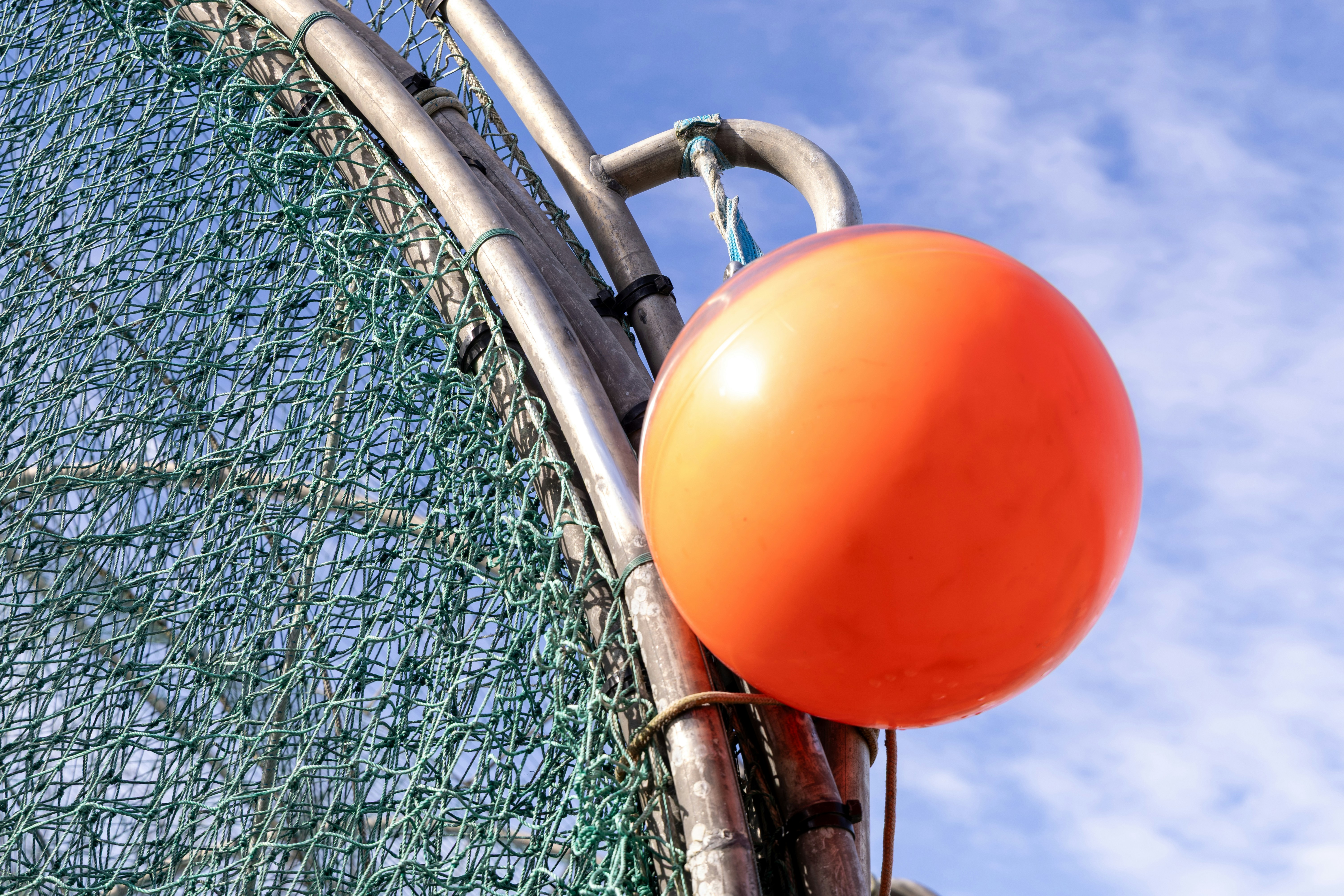 Bright orange ball perched on a weathered fence with blue sky in the background, emphasizing color contrast and geometric arc.